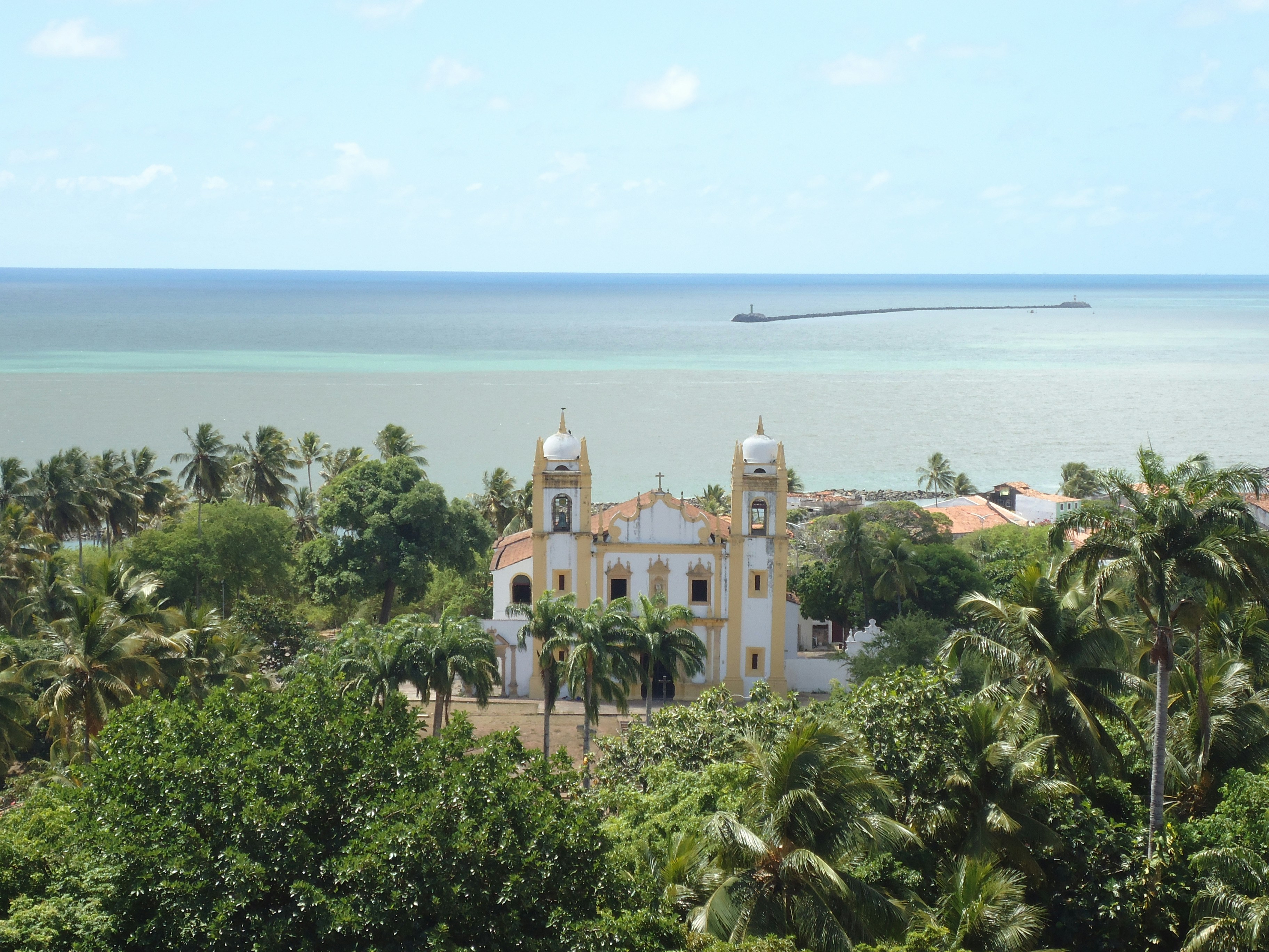 Colonial church nestled in lush greenery with a serene ocean backdrop.