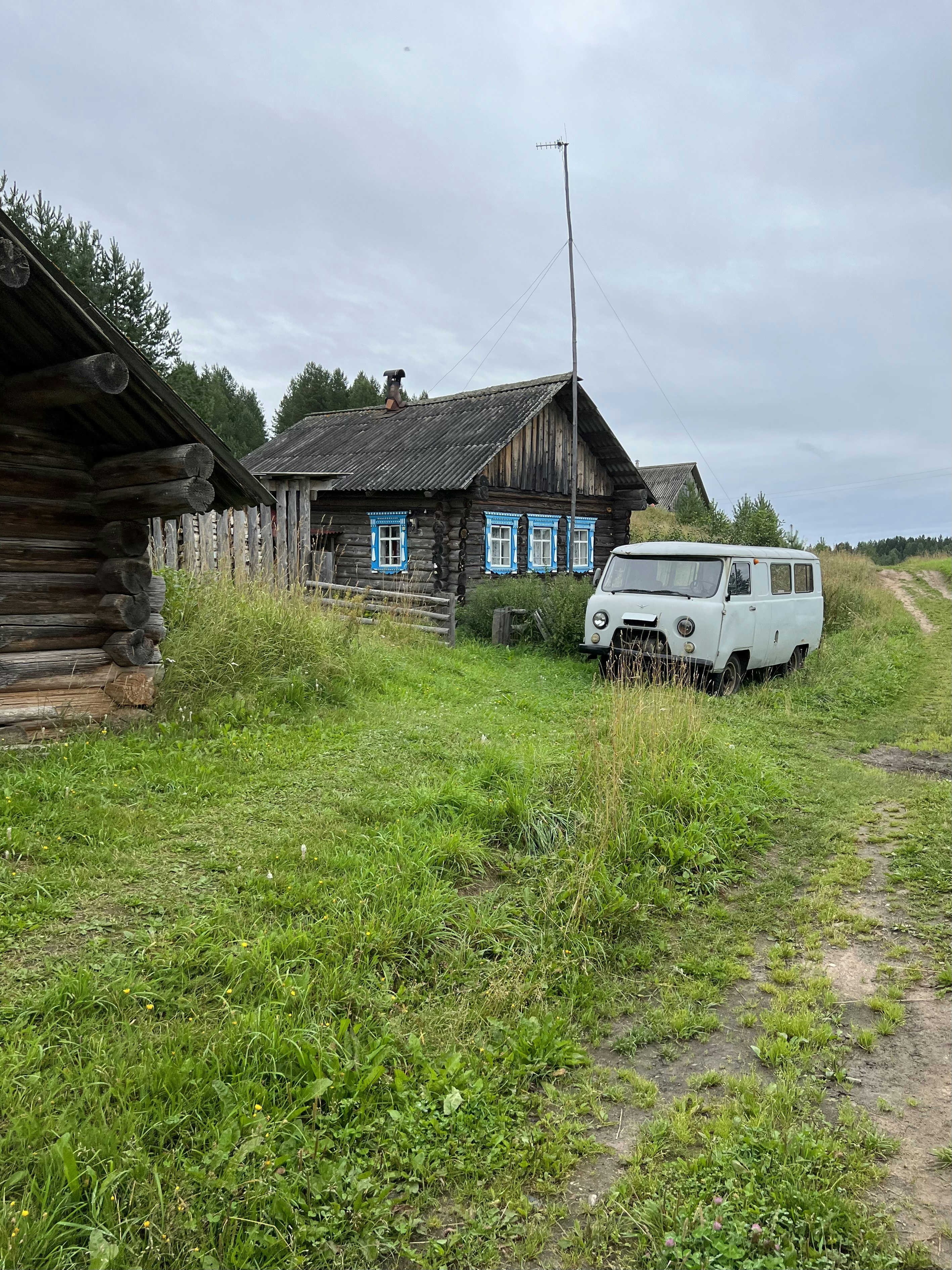 Weathered Lodges, Blue-Windowed Charm, and a Pale Van on a Rural Lane