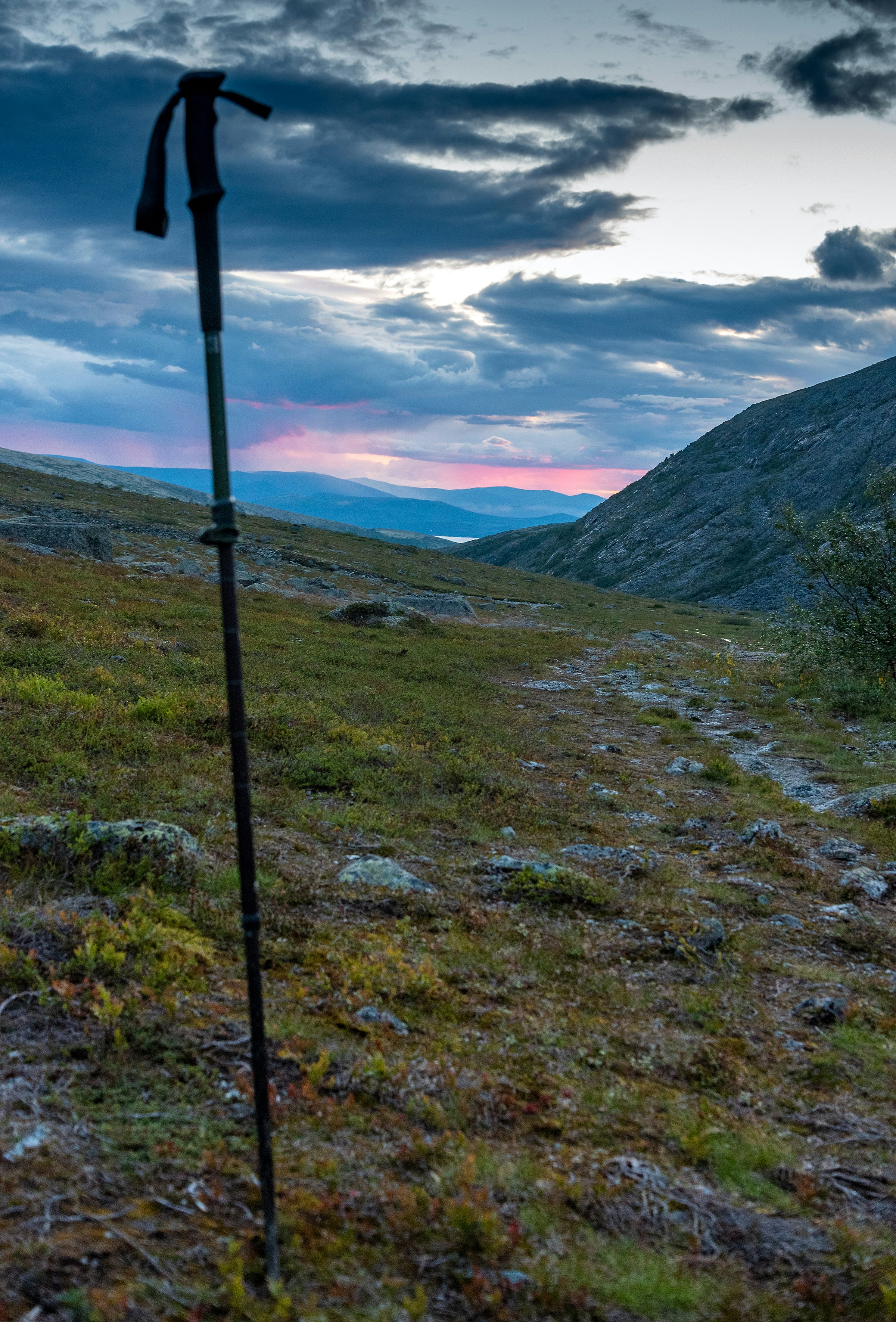 A Lone Trekker’s Pole Reaches for Distant Peaks at Dusk