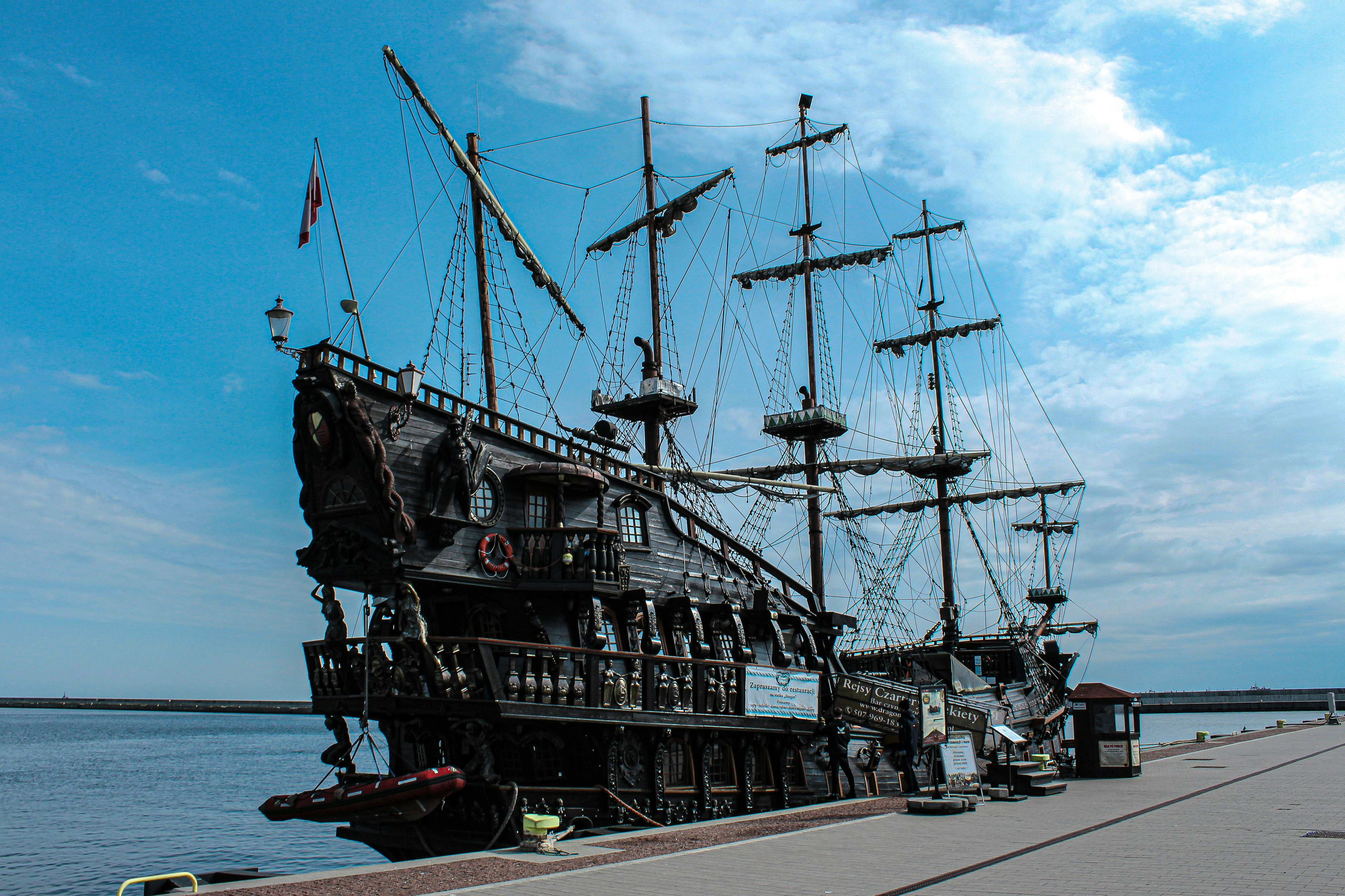 Large wooden pirate ship docked at a sunlit pier beneath a vibrant blue sky.