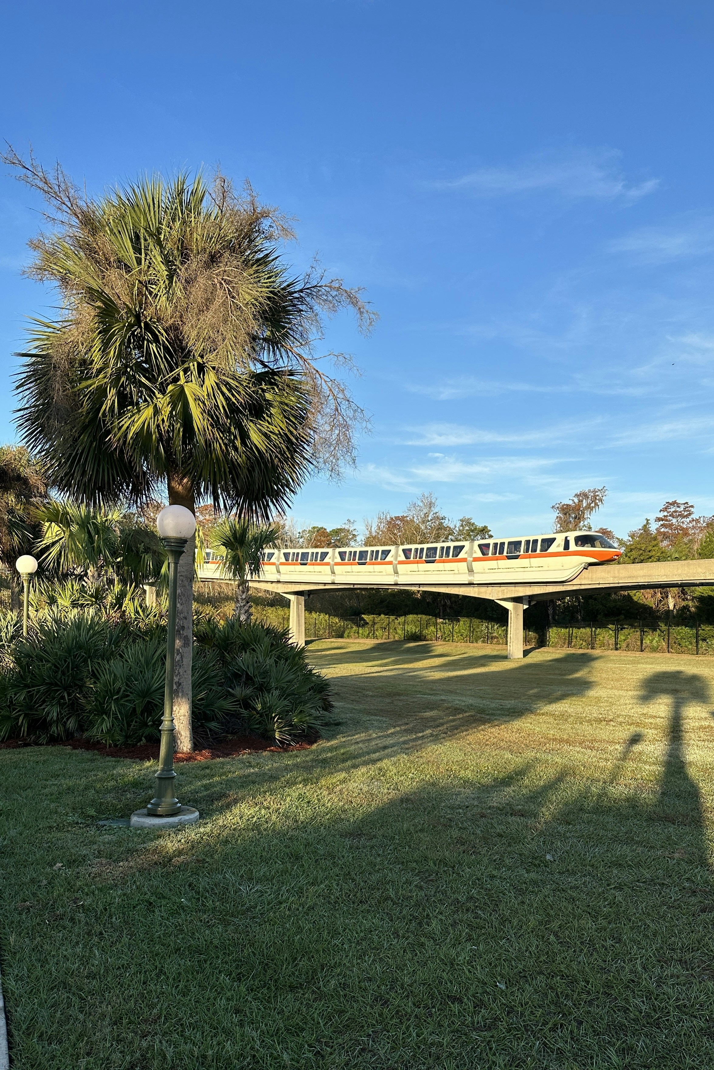 Orange Tram Crossing a Quiet Park Bridge Under a Clear Blue Sky