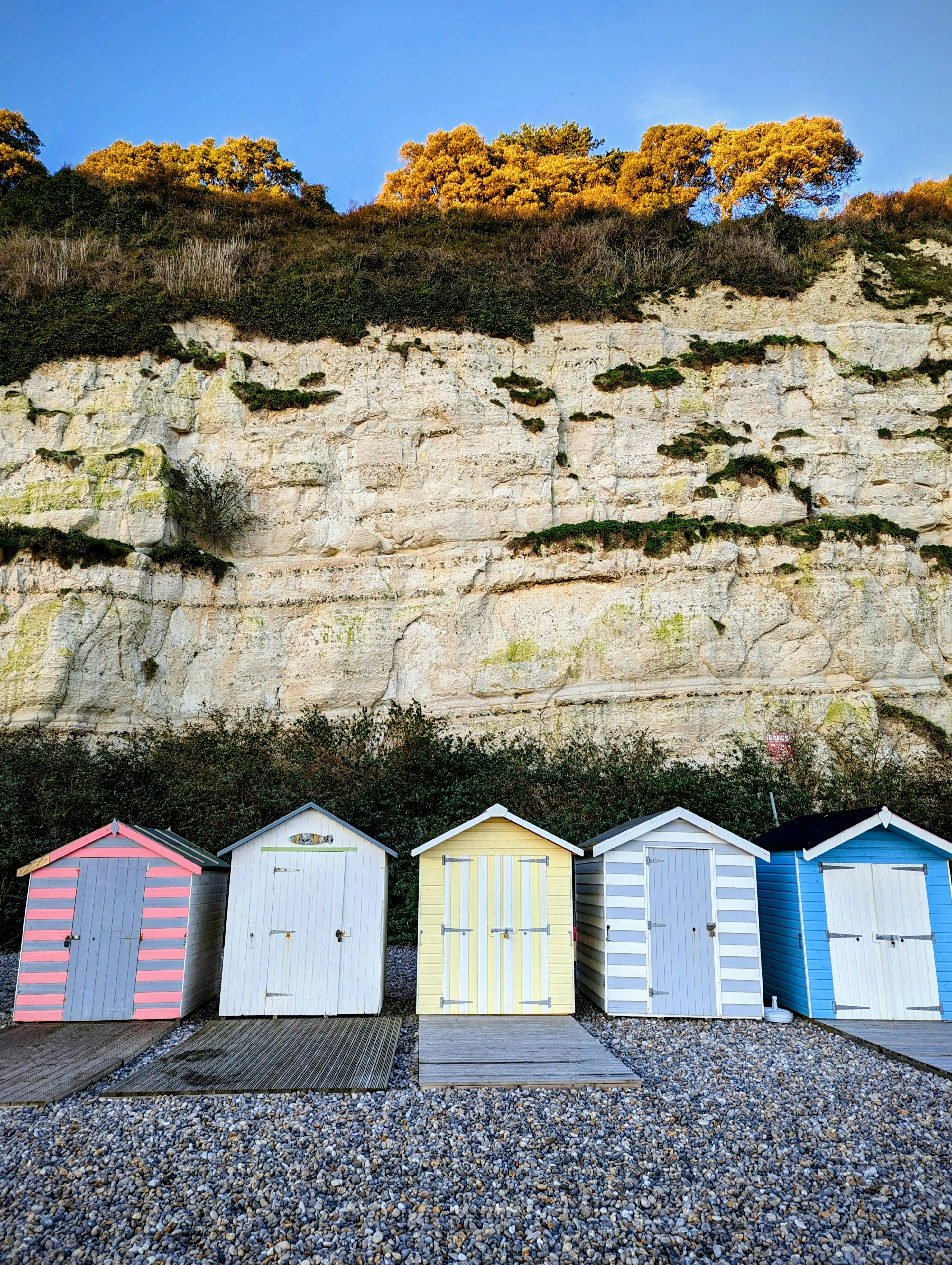 Pastel Row of Beach Huts at the Foot of a Sunlit Chalk Cliff