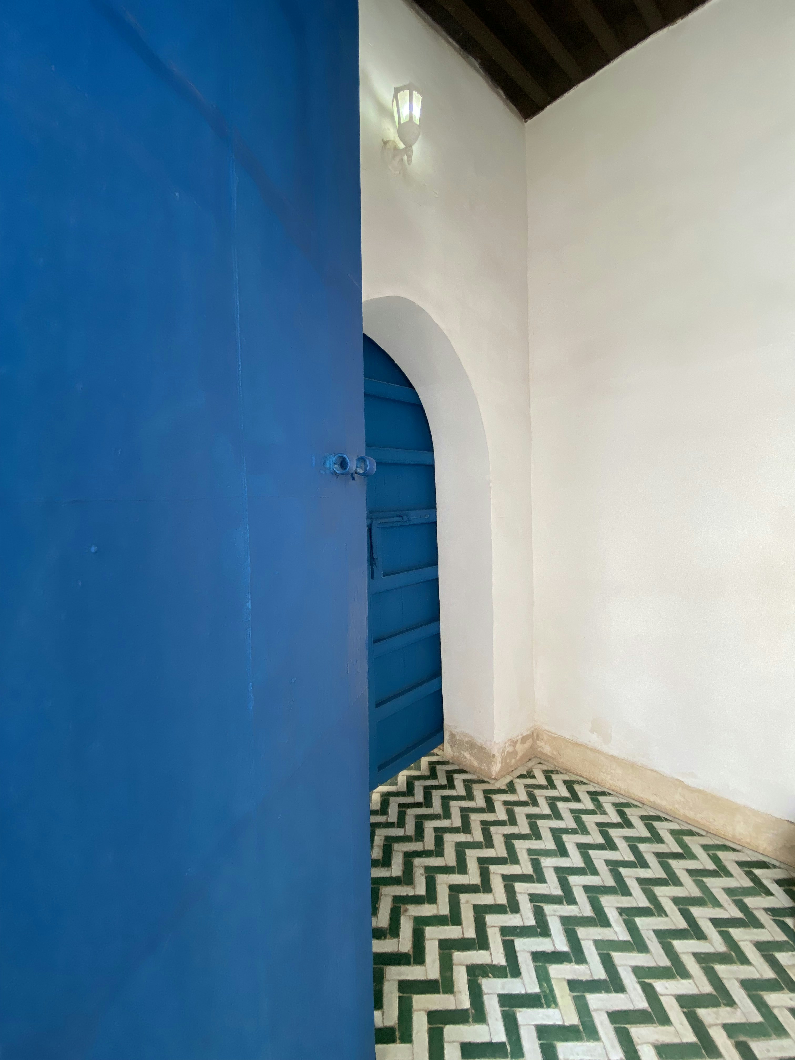 Open blue door leading into a serene interior with patterned green and white tile flooring and a softly lit archway.