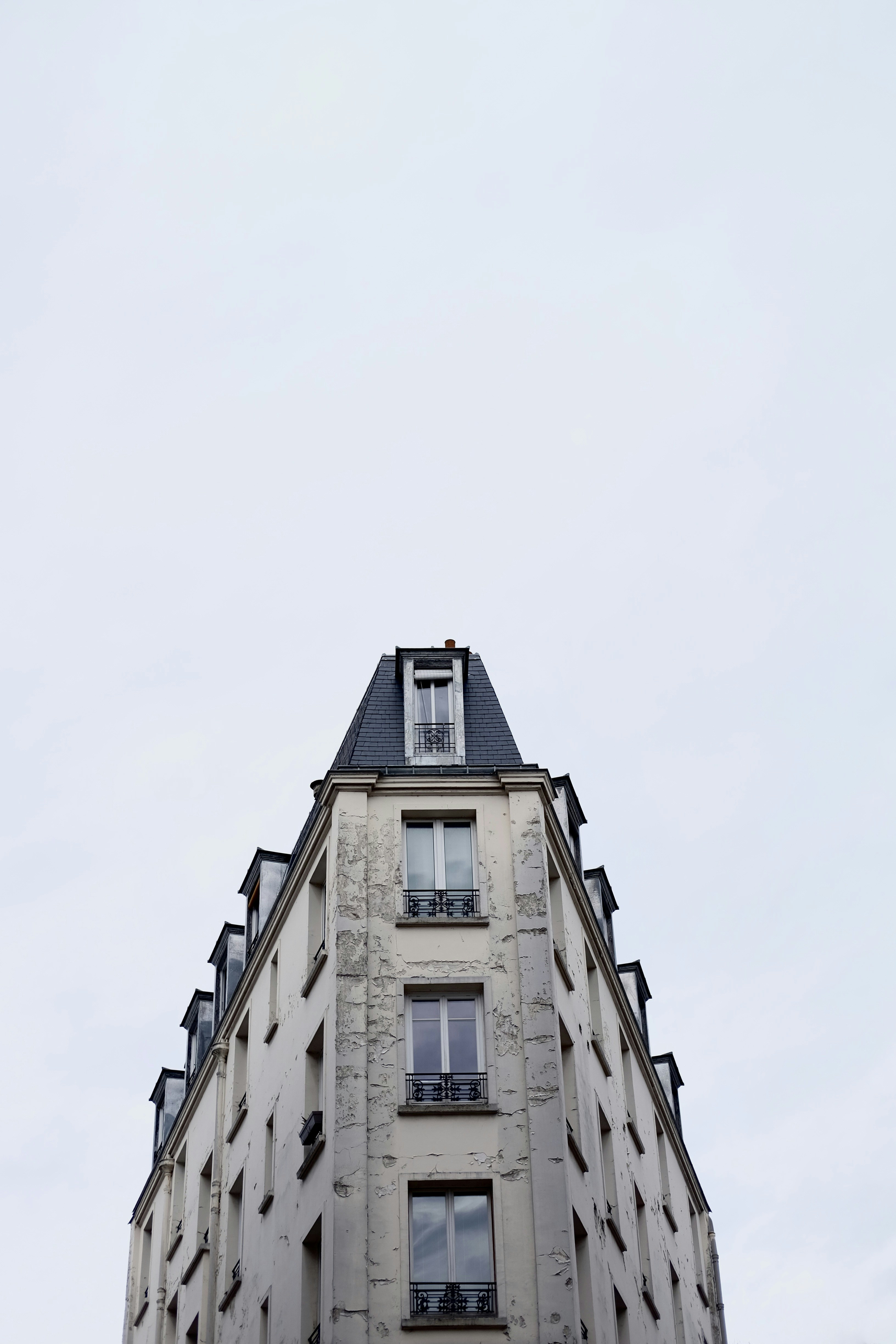 A tall, weathered building reaching towards a gray sky, showcasing intricate window details and a distinct roofline.