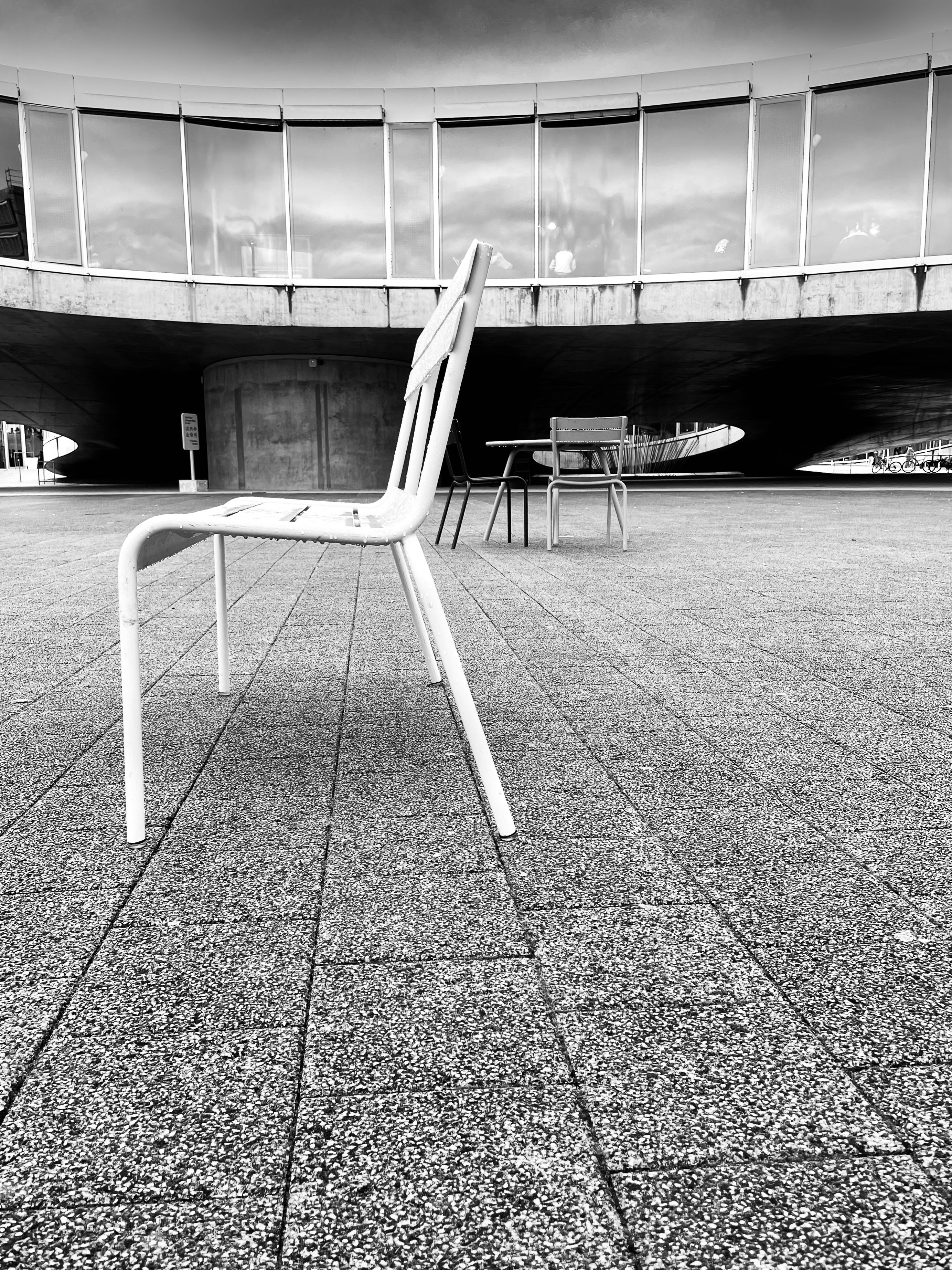 Tilted Chair Against a Curved Glass Backdrop: A Study in Urban Geometry