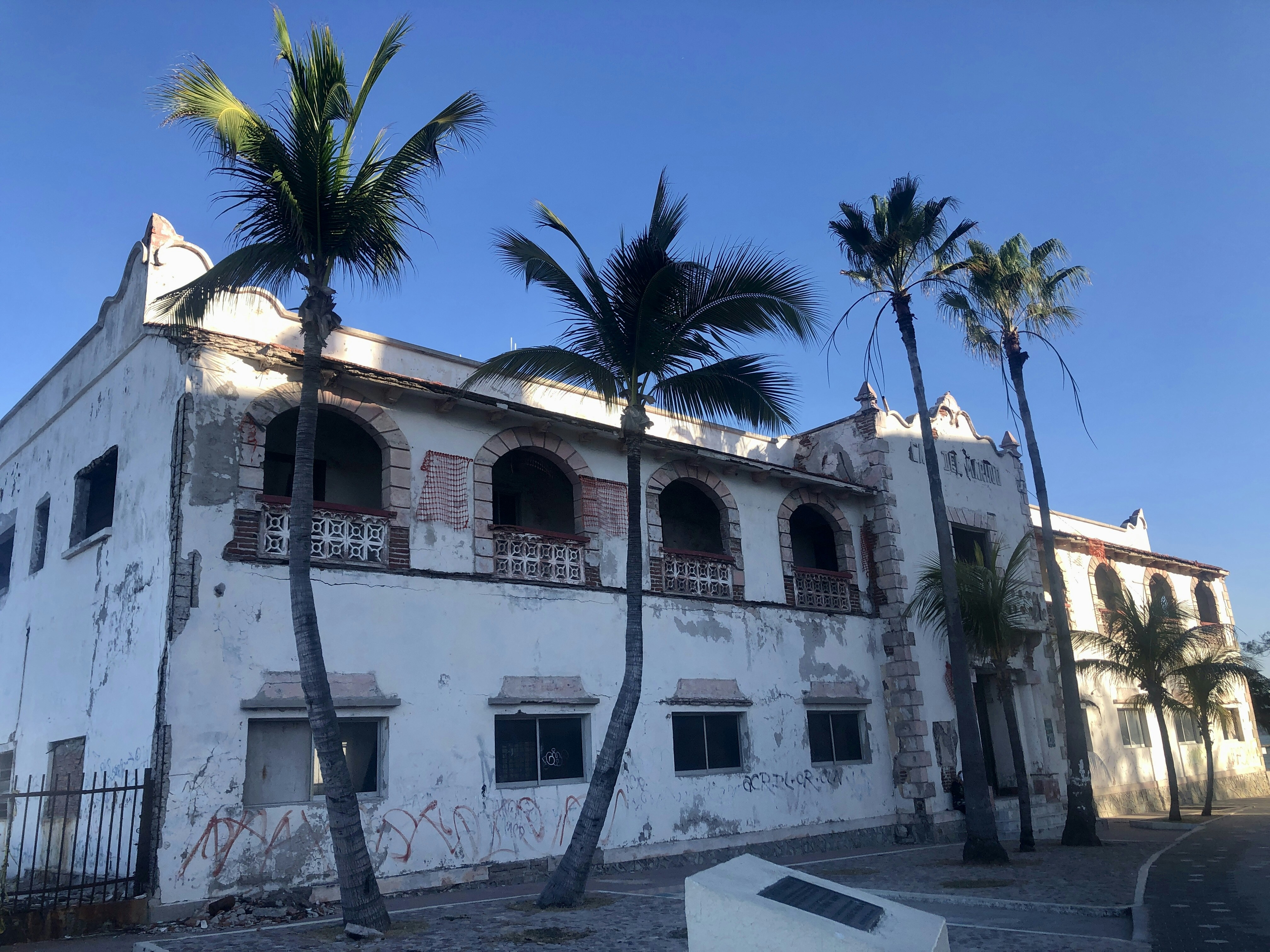 Old white building with arched balconies and tall palm trees against a clear blue sky.