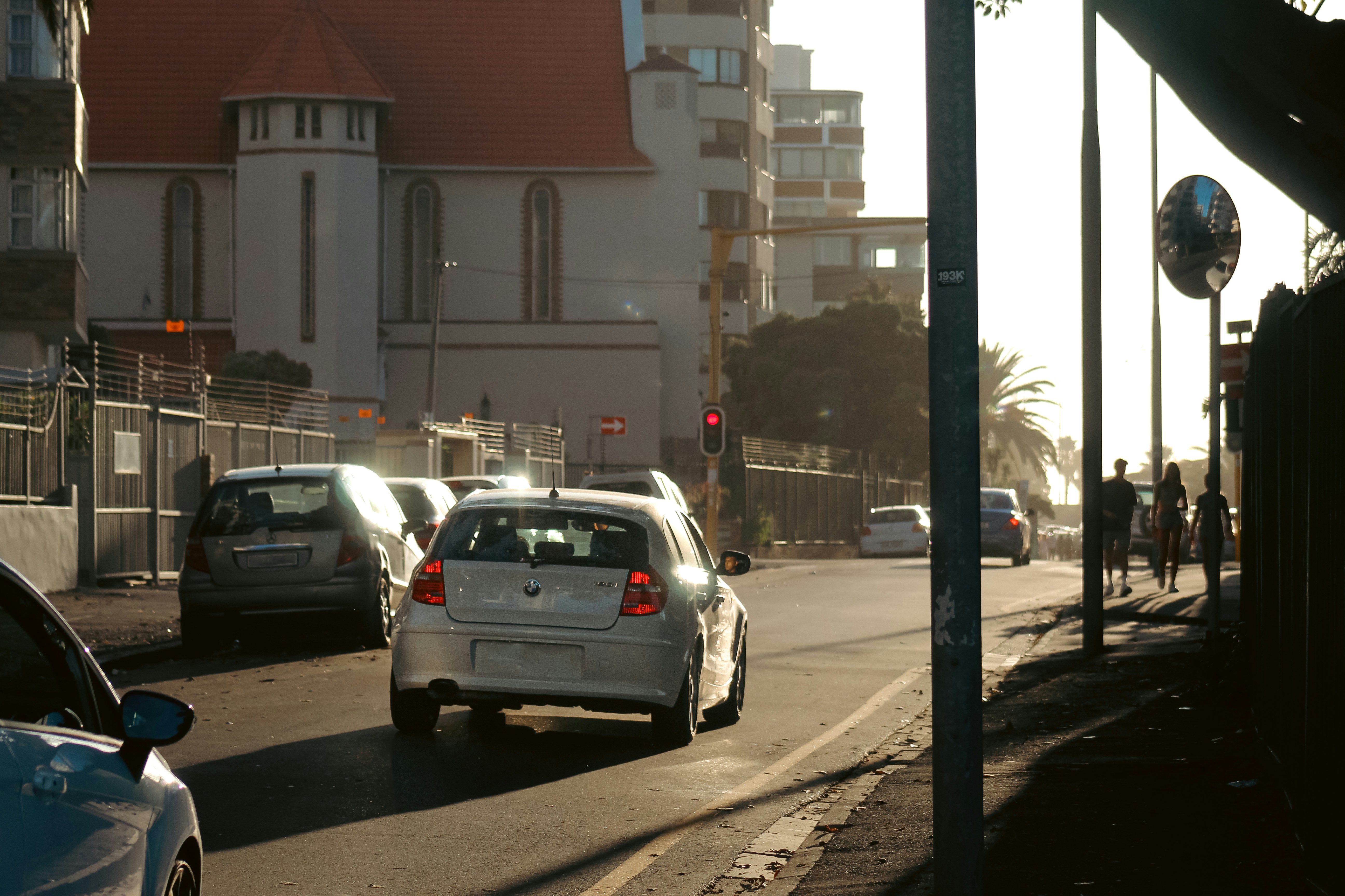 Sunlit Street Currents: The White Hatchback Anchors a Quiet Evening Run