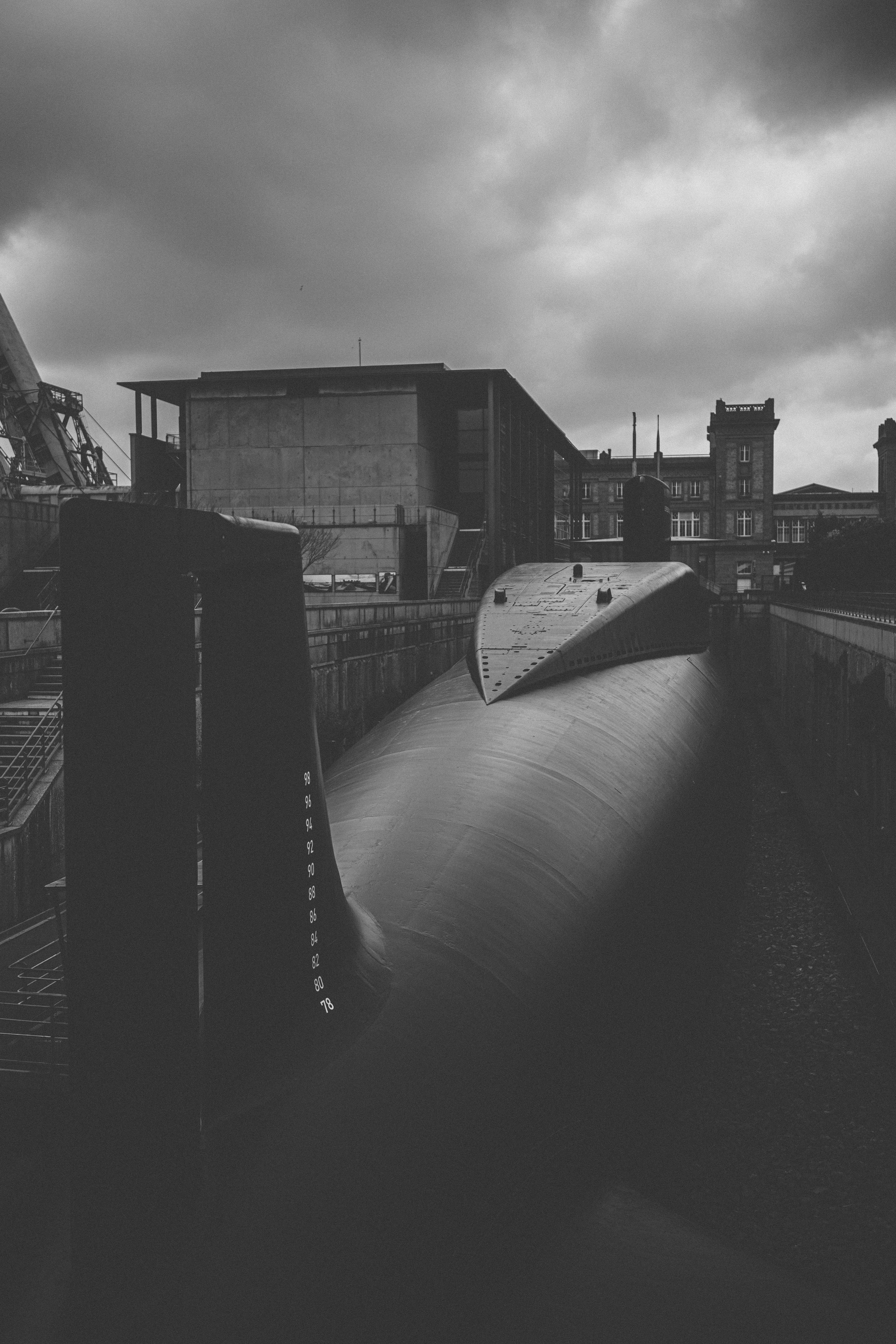 Black and white photo of a submarine in a dockyard under a cloudy sky.