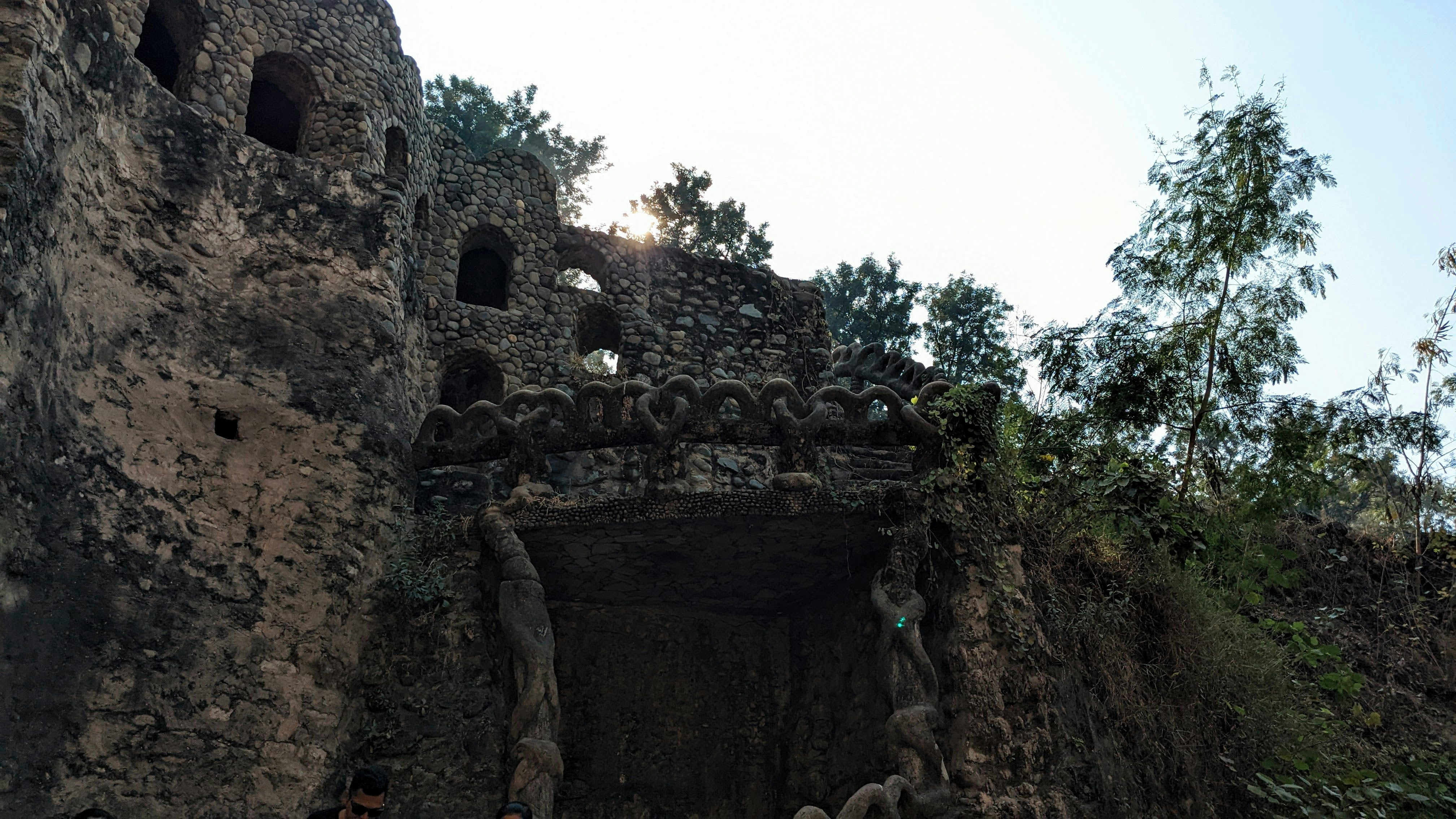 Ancient stone structure with arched openings surrounded by lush greenery under a clear sky.
