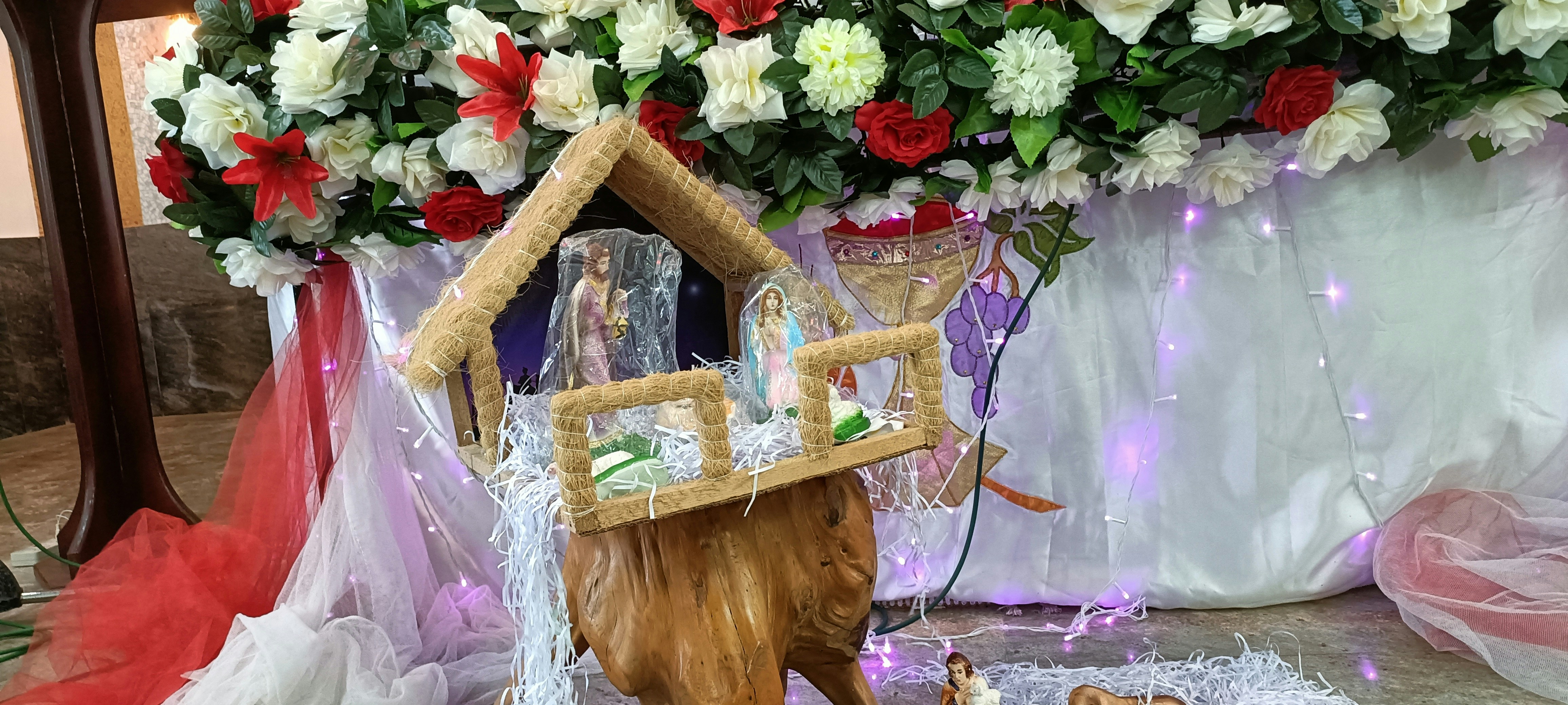 Intricately designed nativity scene featuring a stable and figurines, adorned with vibrant flowers and soft lighting.