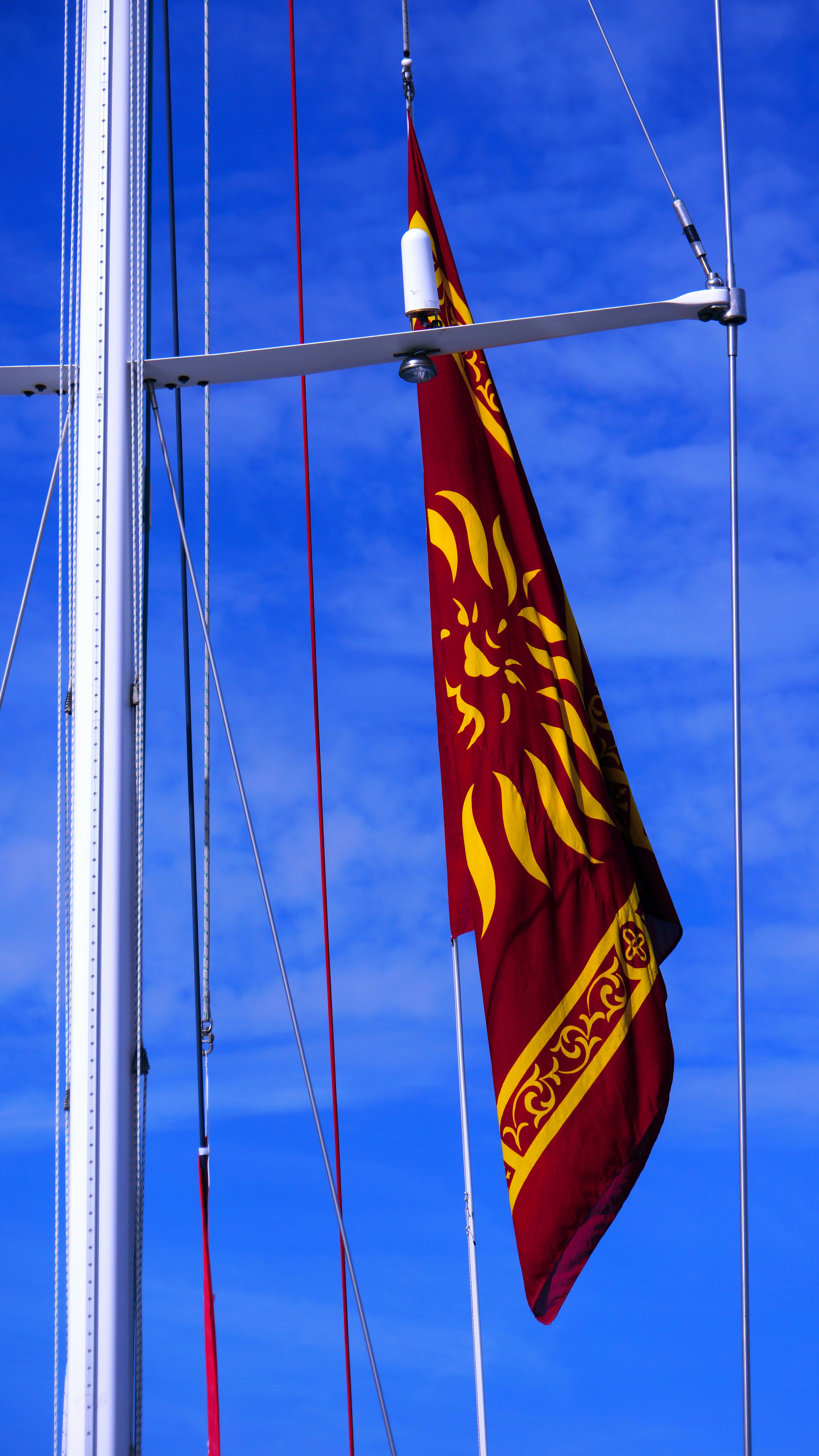 Crimson Sunburst Flag Framed by Rigging Against a Cerulean Sky
