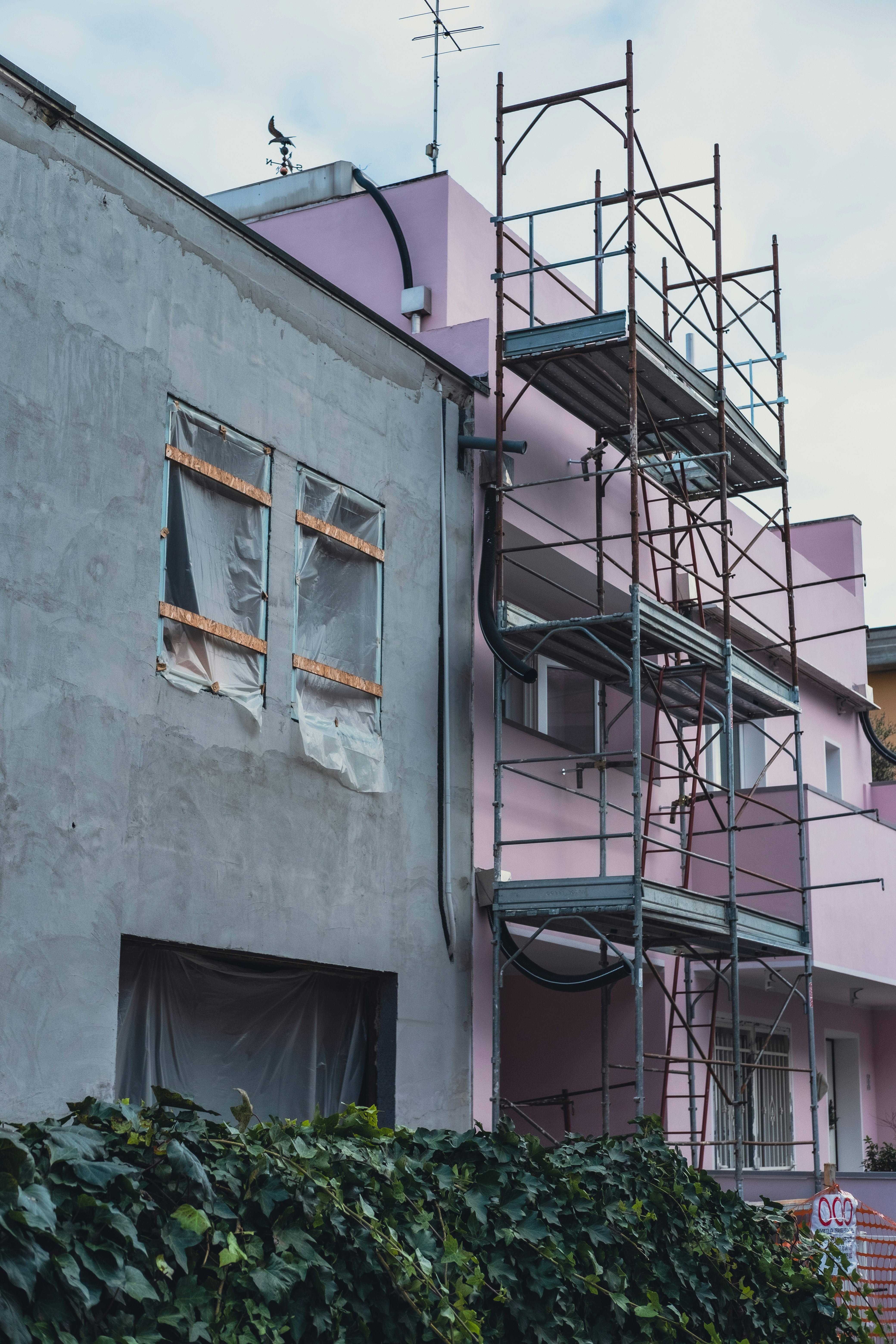 Pastel Scaffold: Ivy-Framed Urban Renovation Against a Pink Facade