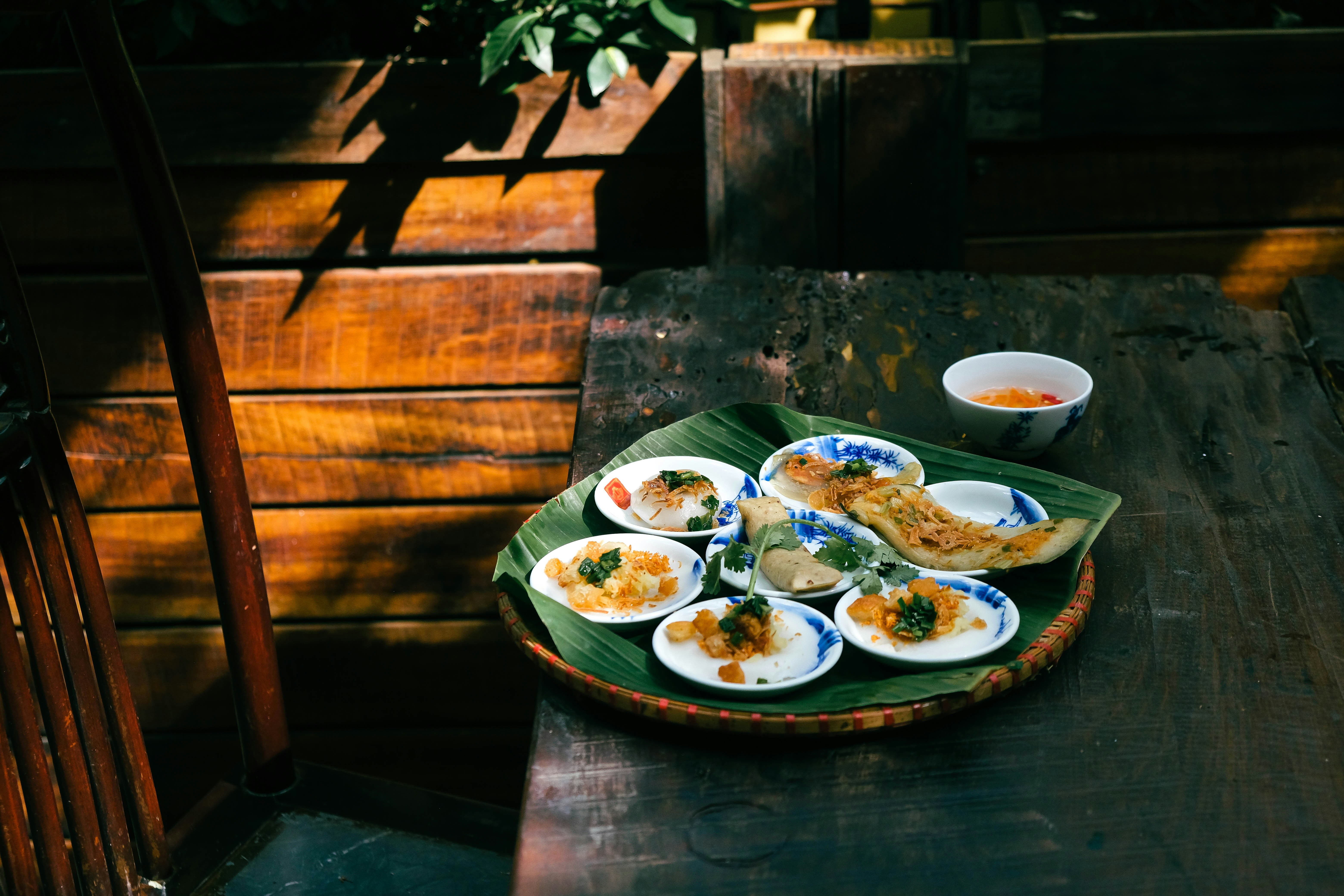Sunlit Banana-Leaf Tray of Small Plates on Weathered Wood