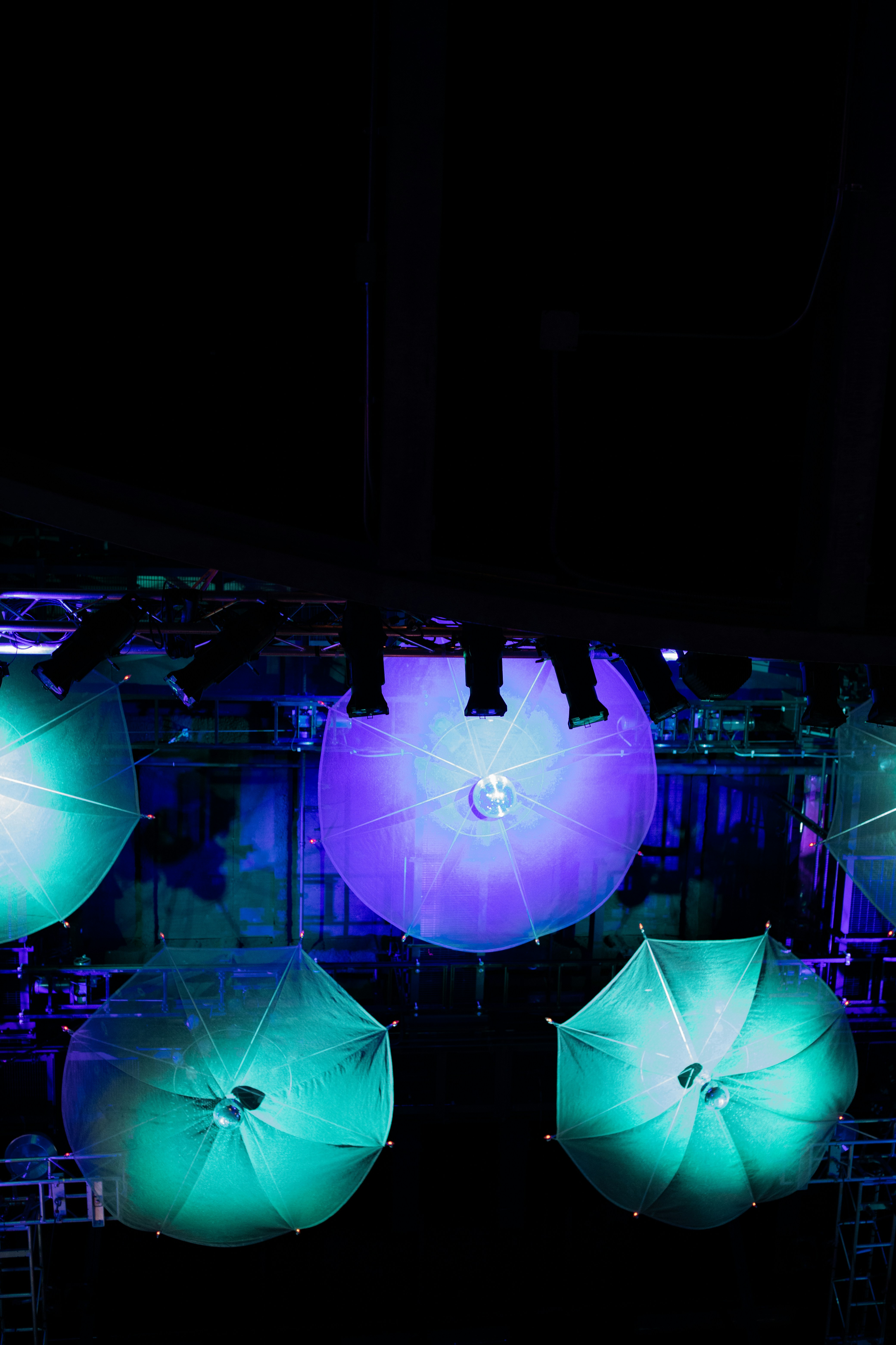 Colorful illuminated canopies suspended from above, casting vibrant shadows in a darkened venue.