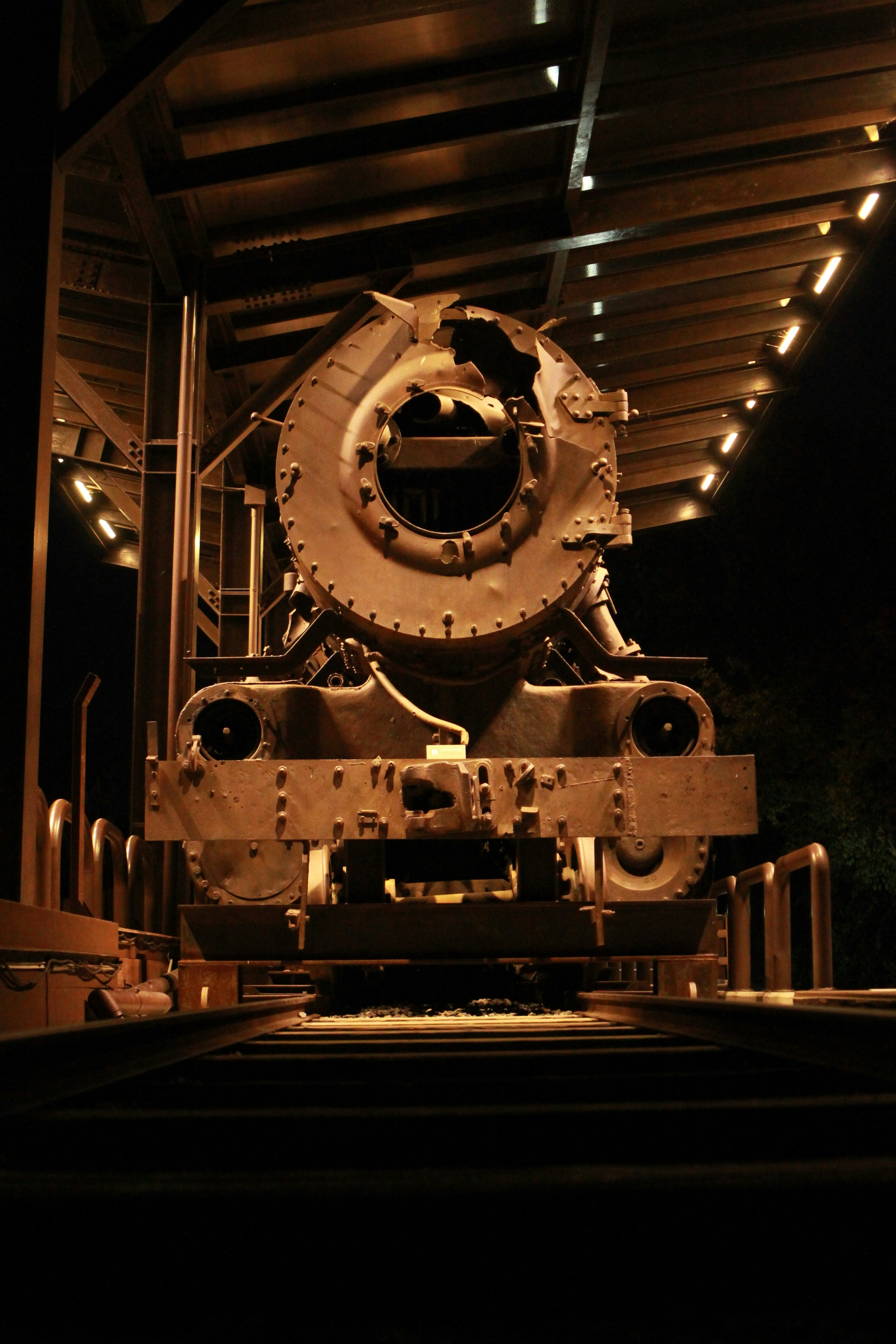 Rusty vintage steam locomotive illuminated under a metallic canopy at night, showcasing its intricate details and textures.