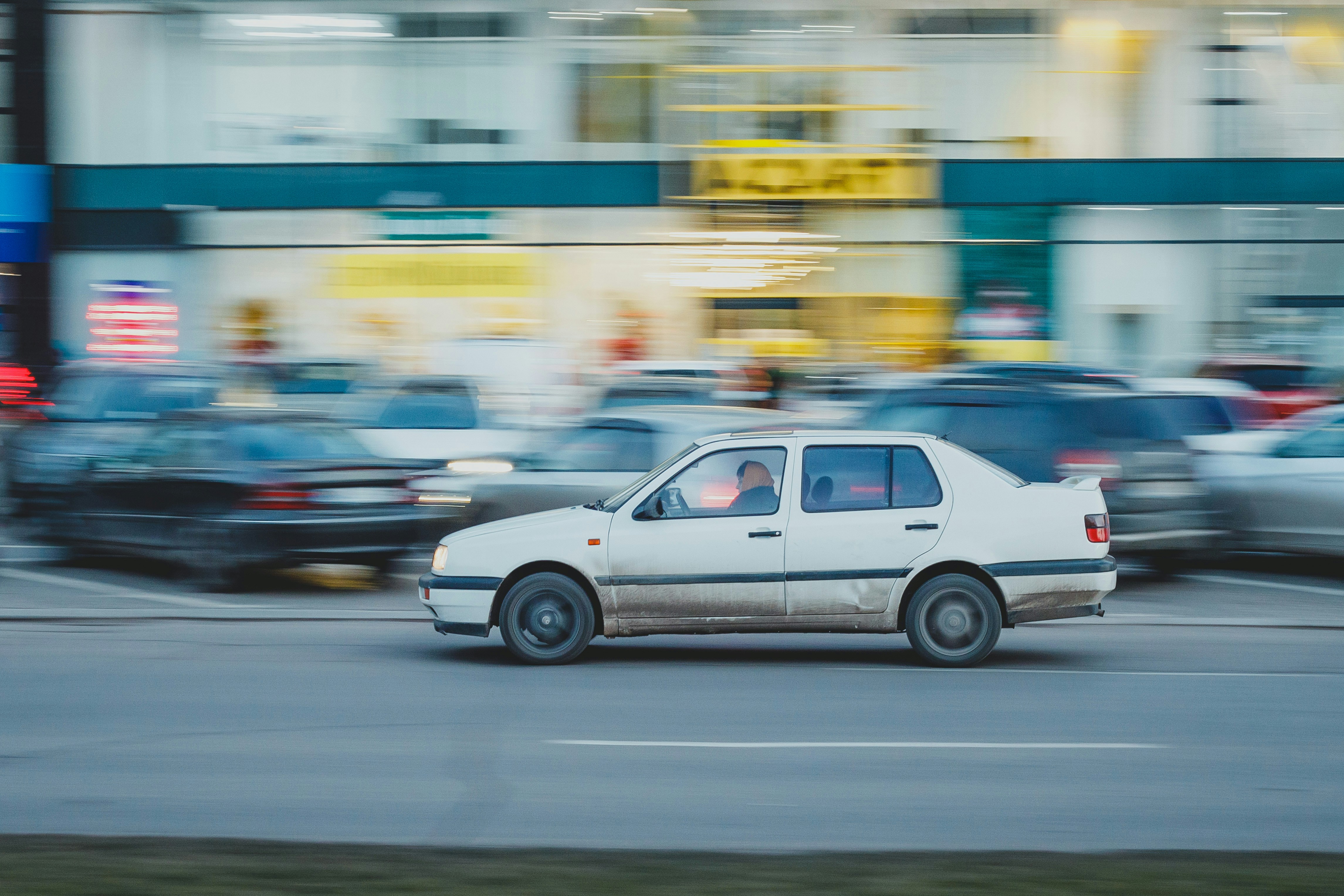 A white car driving down a street next to a tall building photo – Free ...