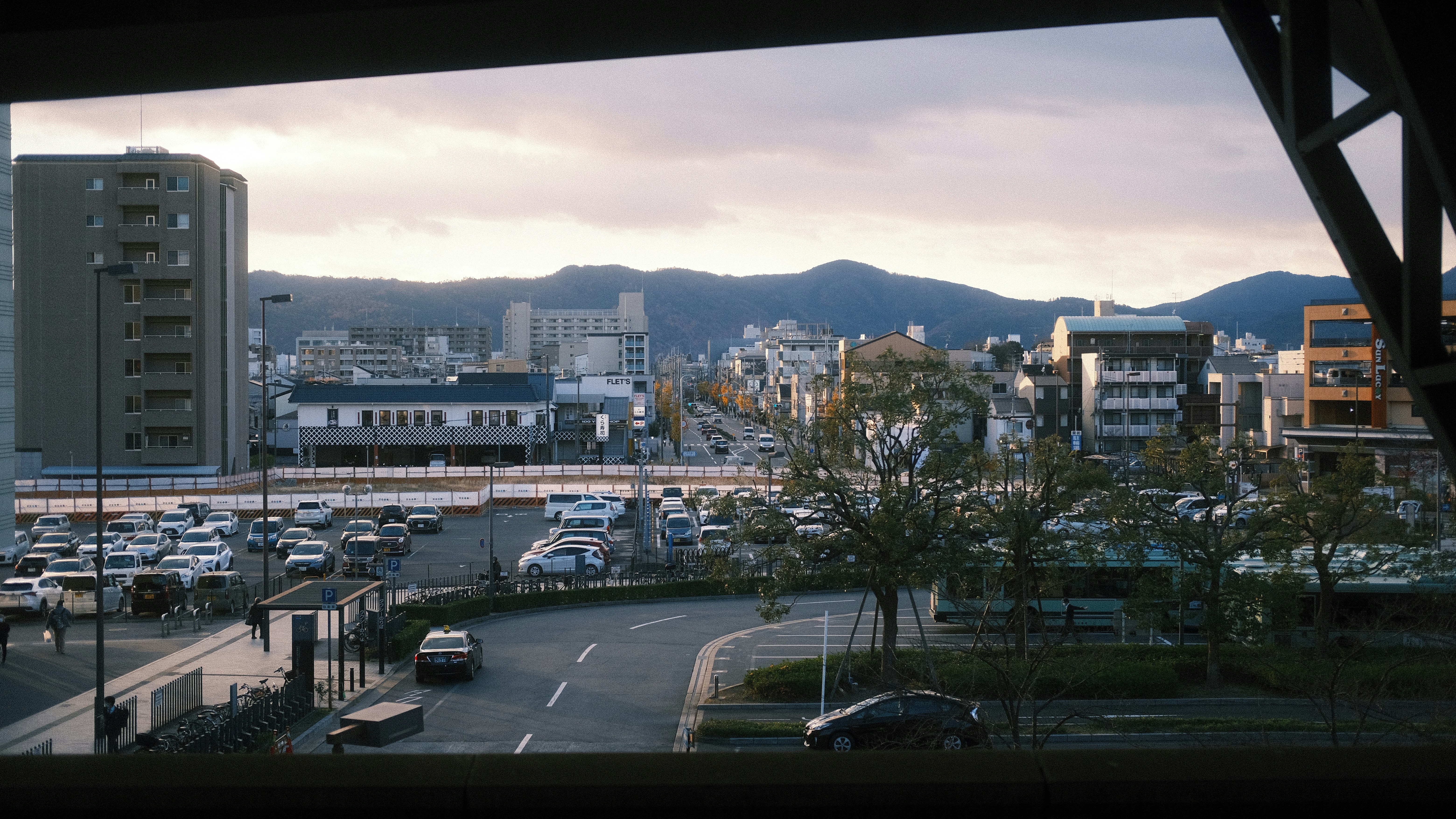 Windowed Cityscape at Dusk: Parking Lots, Streets, and a Mountain Horizon