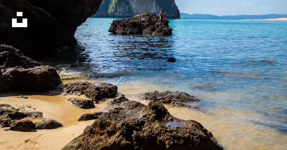 Un Hombre Parado En La Cima De Una Playa De Arena Junto Al Océano Foto