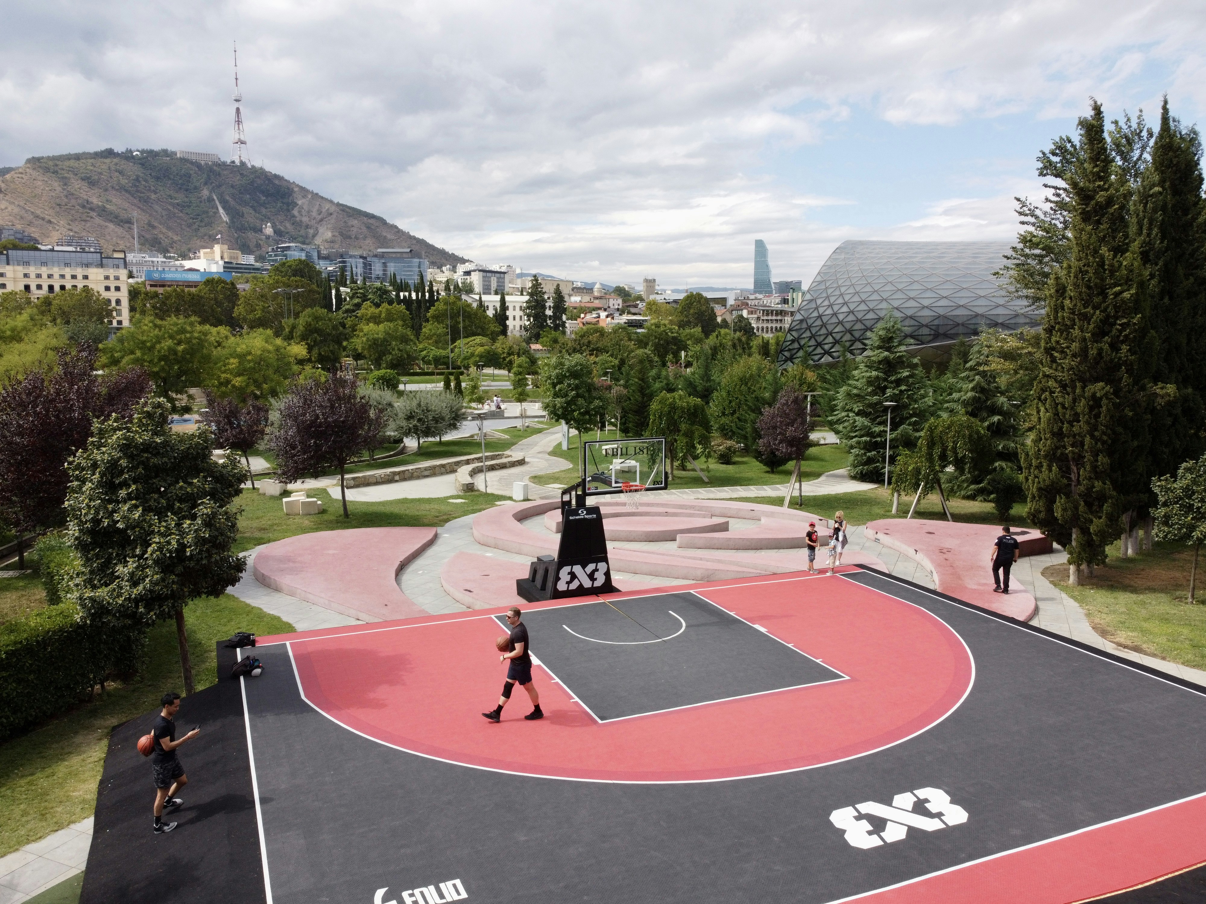 Red-Court Play in a City Park: Green Canopy and Distant Skyline