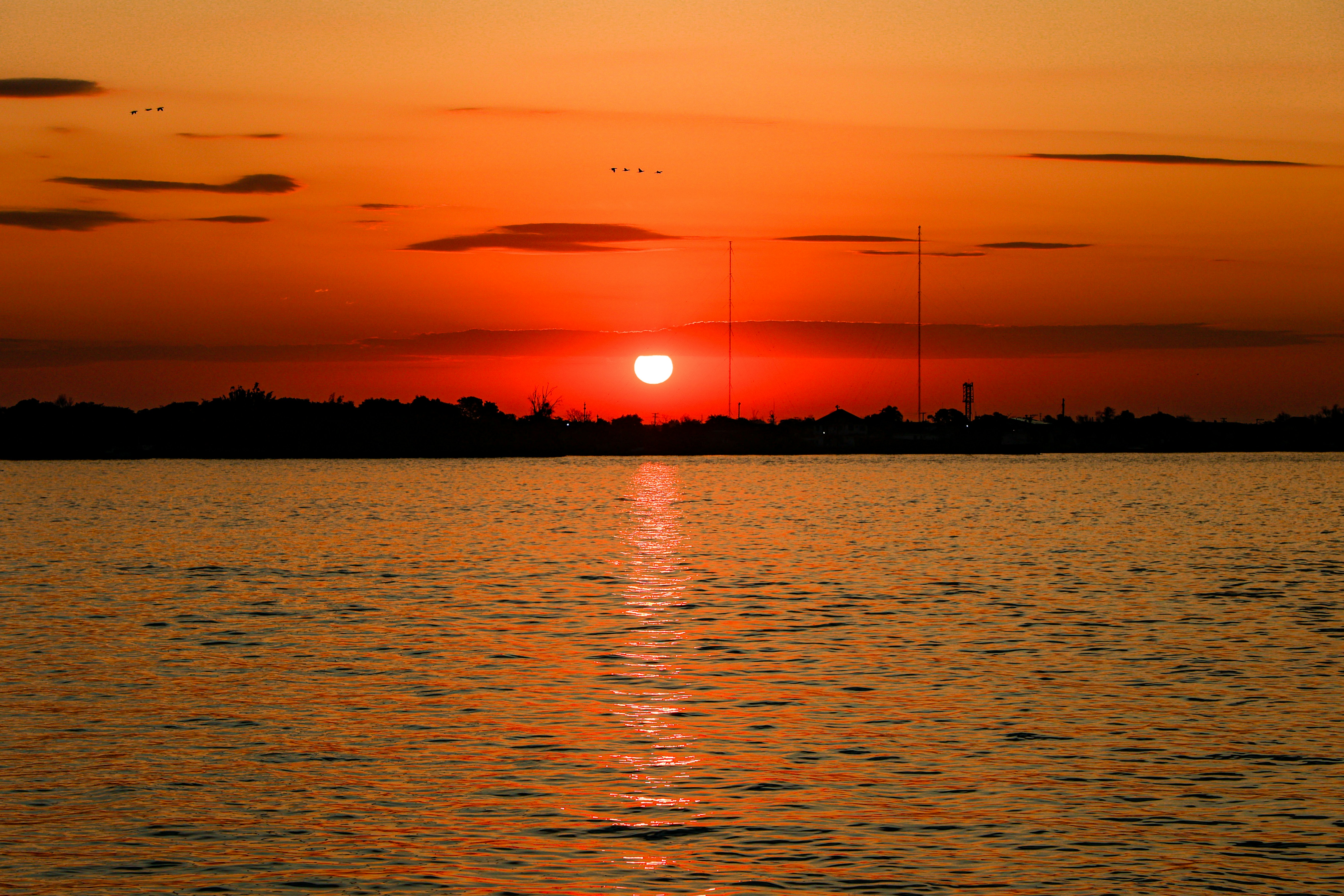 Sun setting over a calm lake with a vibrant red sky and silhouetted shoreline.