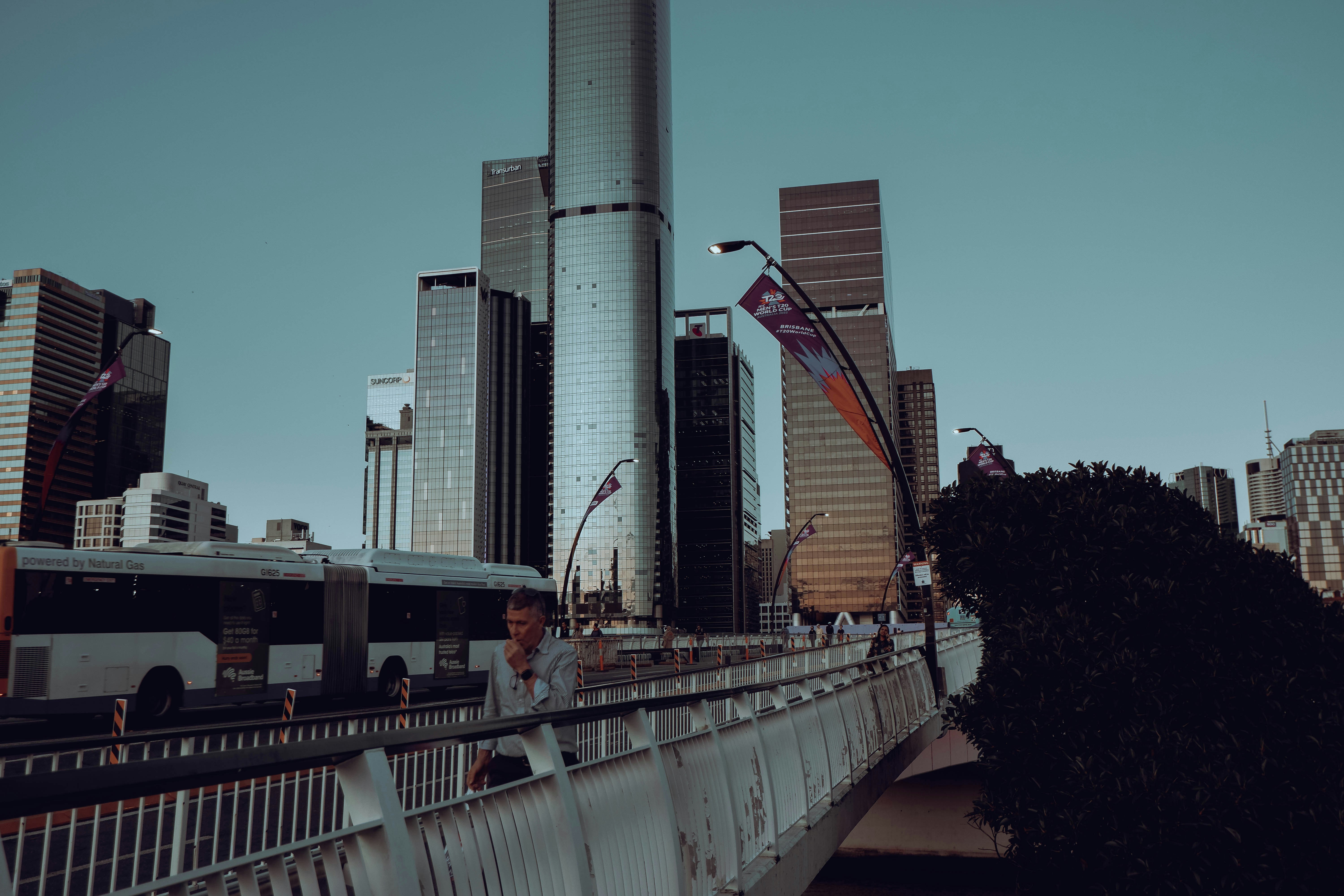 A pedestrian bridge in a bustling city, framed by towering skyscrapers and city buses, creates a vibrant urban atmosphere.