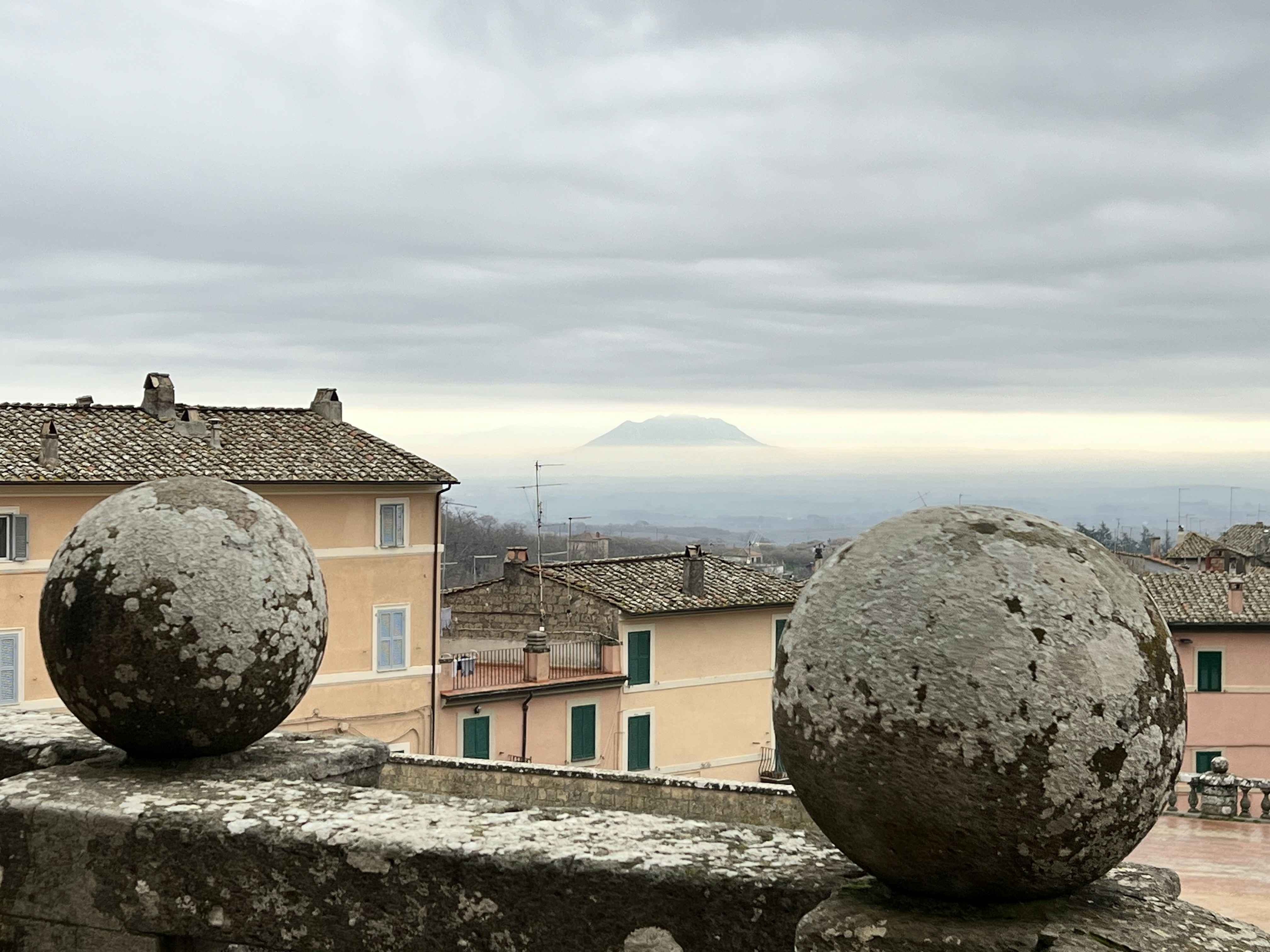 Spherical Sentinels Over a Quiet Terrace as a Hazy Volcano Rises on the Horizon