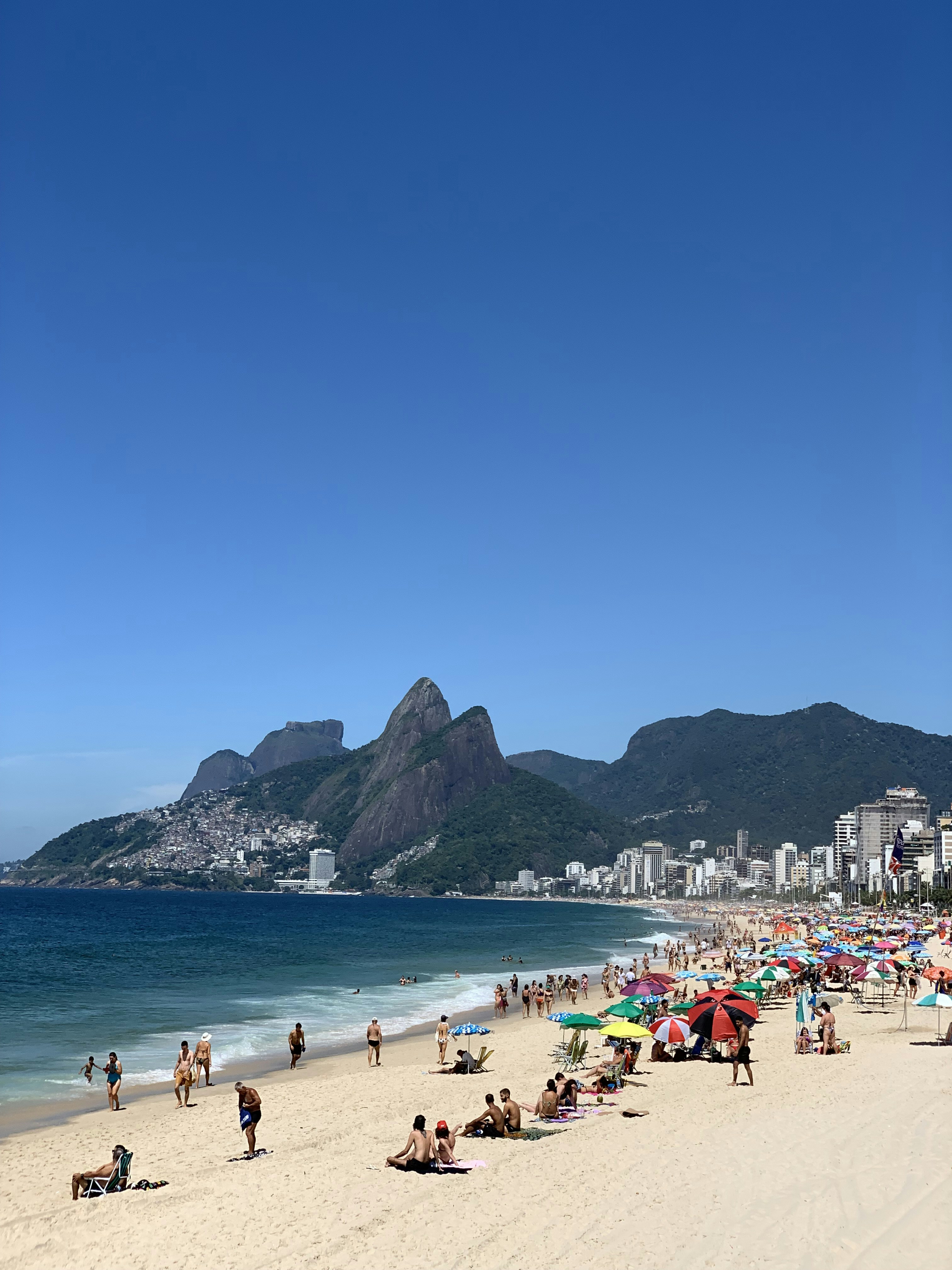 Coastal Cityscape: Umbrella-lined Beach with a Backdrop of Lush Peaks