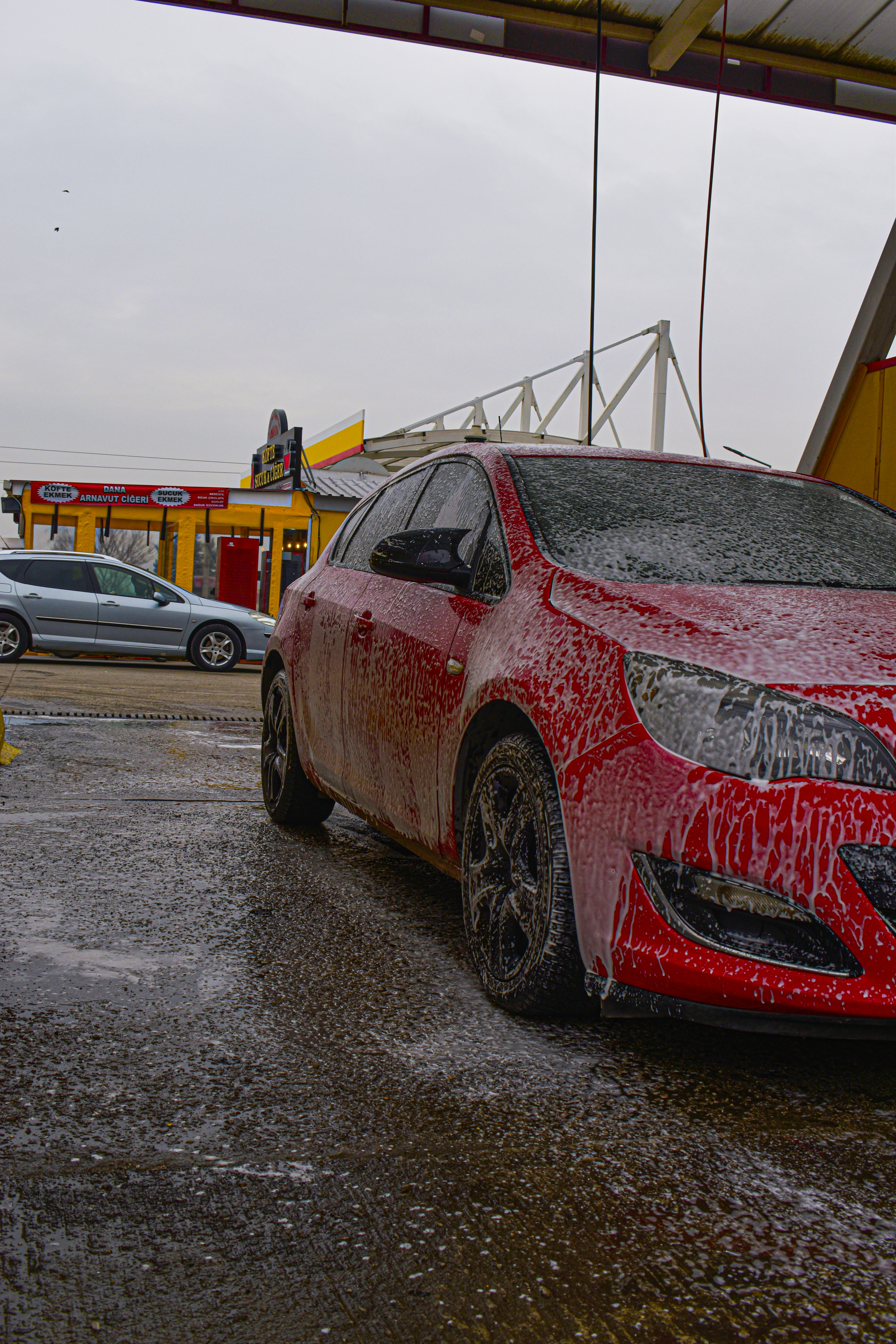 Foamy Red Hatchback at a Busy Car Wash: A Moment of Wet Detail
