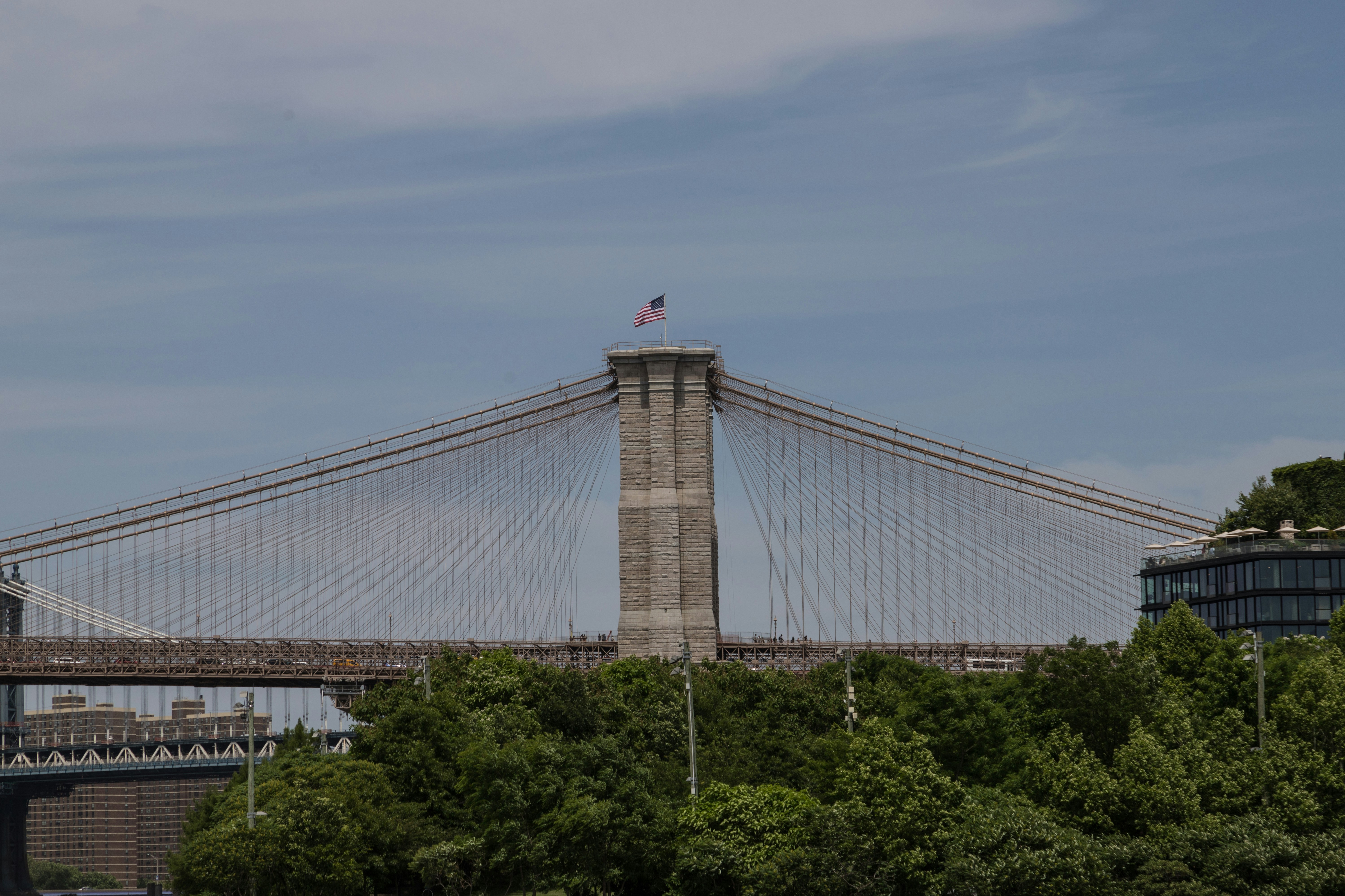 Flag-Topped Suspension Bridge Tower Rising Over a Lush Riverside