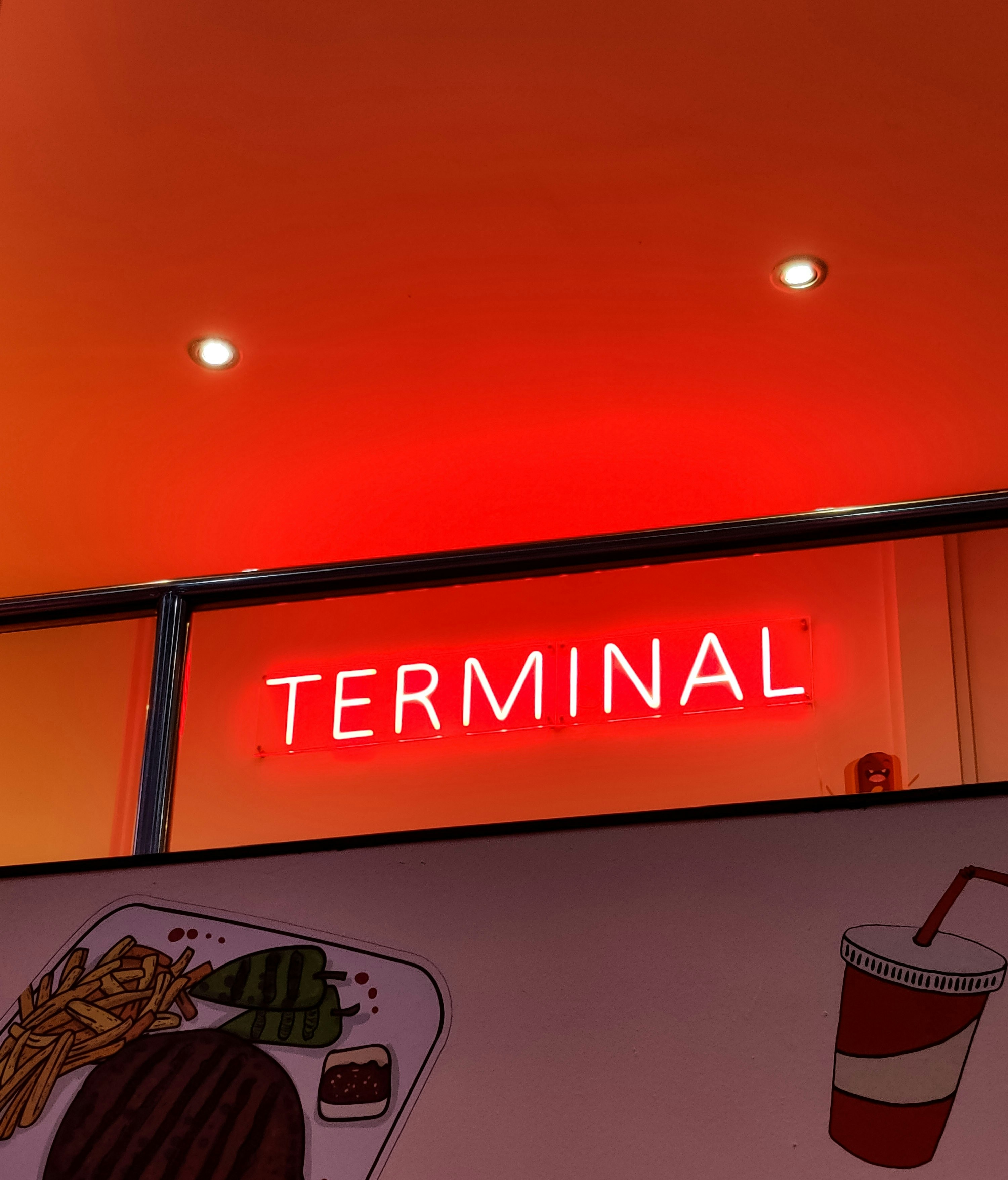 Neon sign reading 'TERMINAL' illuminated against a vibrant background, accompanied by a colorful food illustration below.