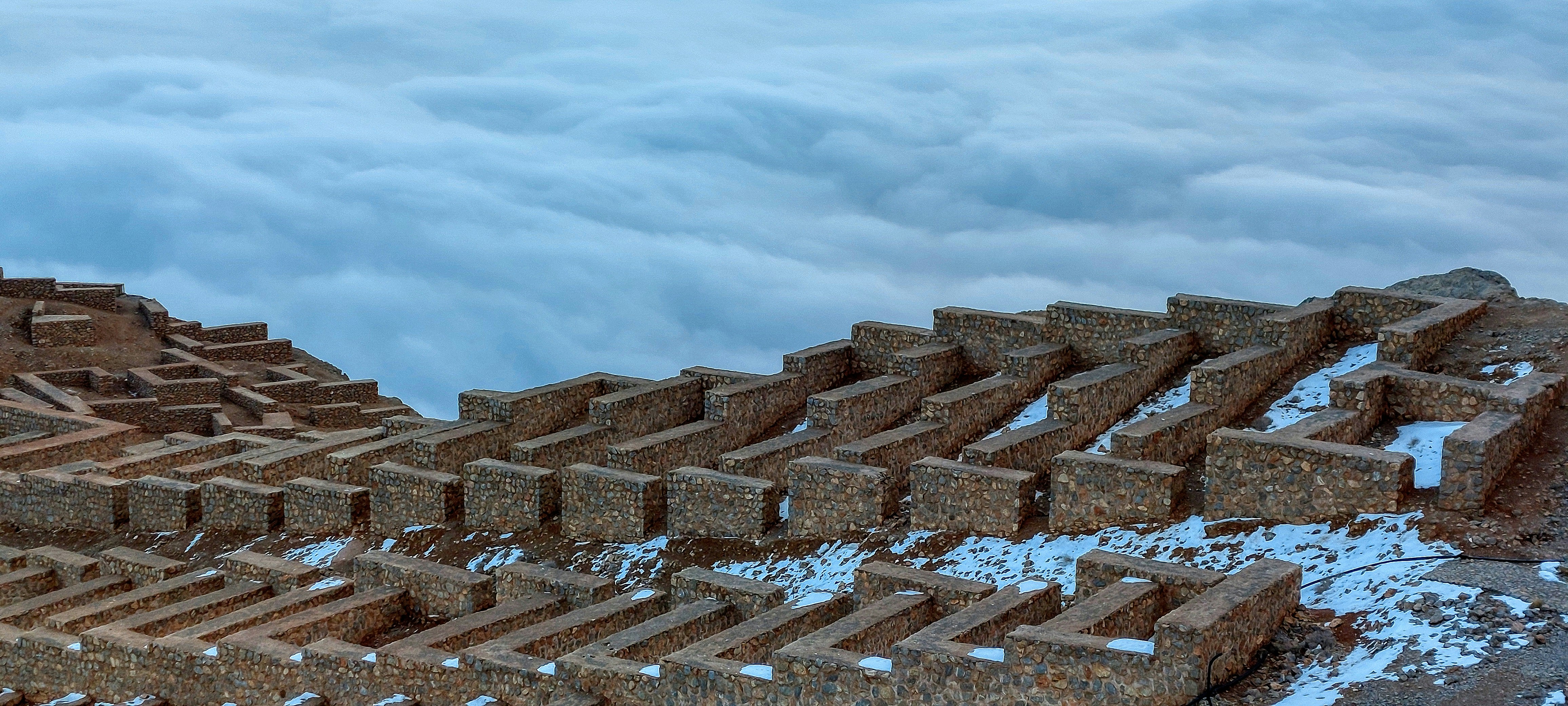 Stone ruins of a historical fortress atop Sefe Mountain, partially covered in snow, with a backdrop of cloud-filled sky.