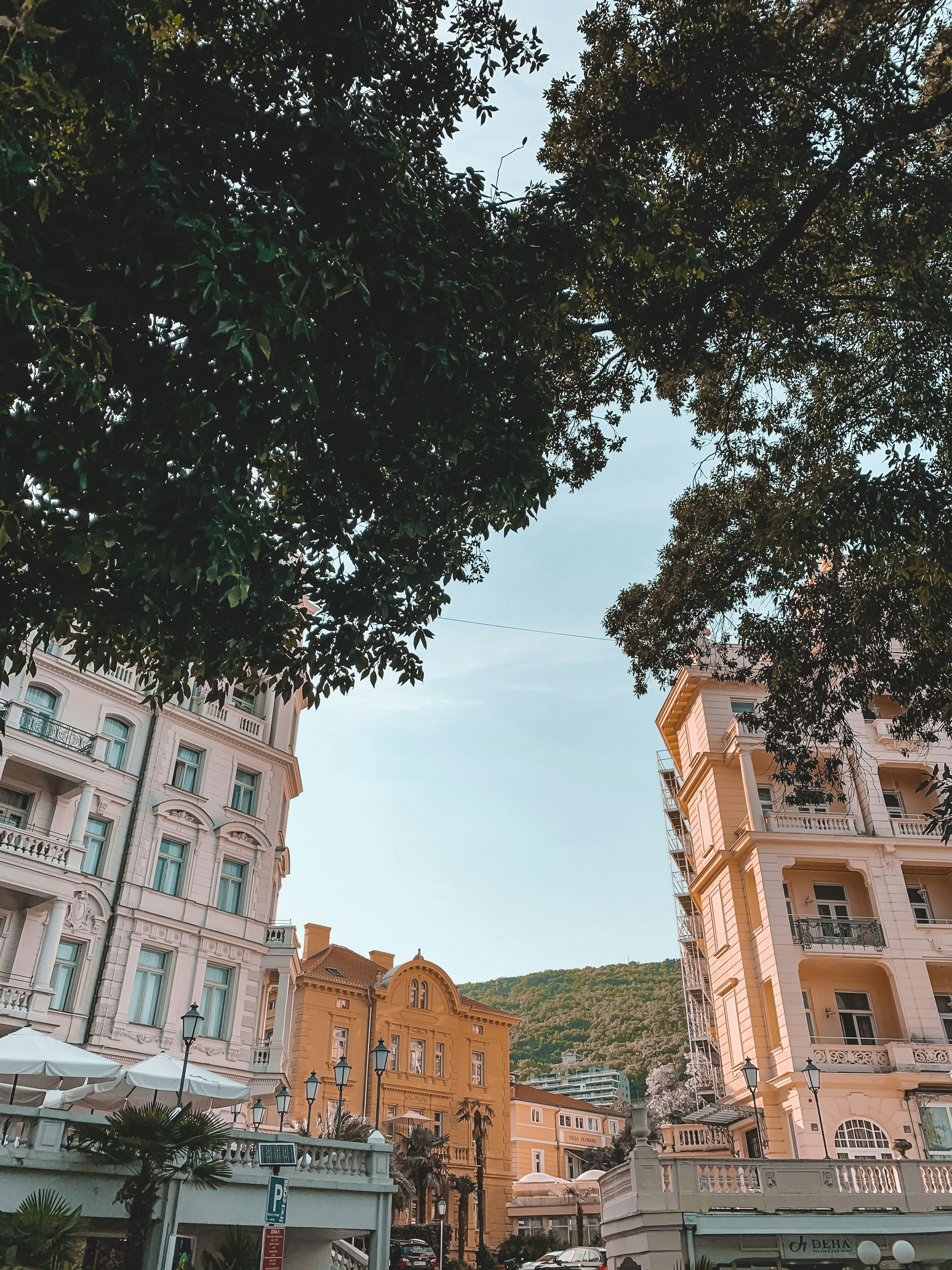 Sunlit street between pastel façades framed by leafy arches