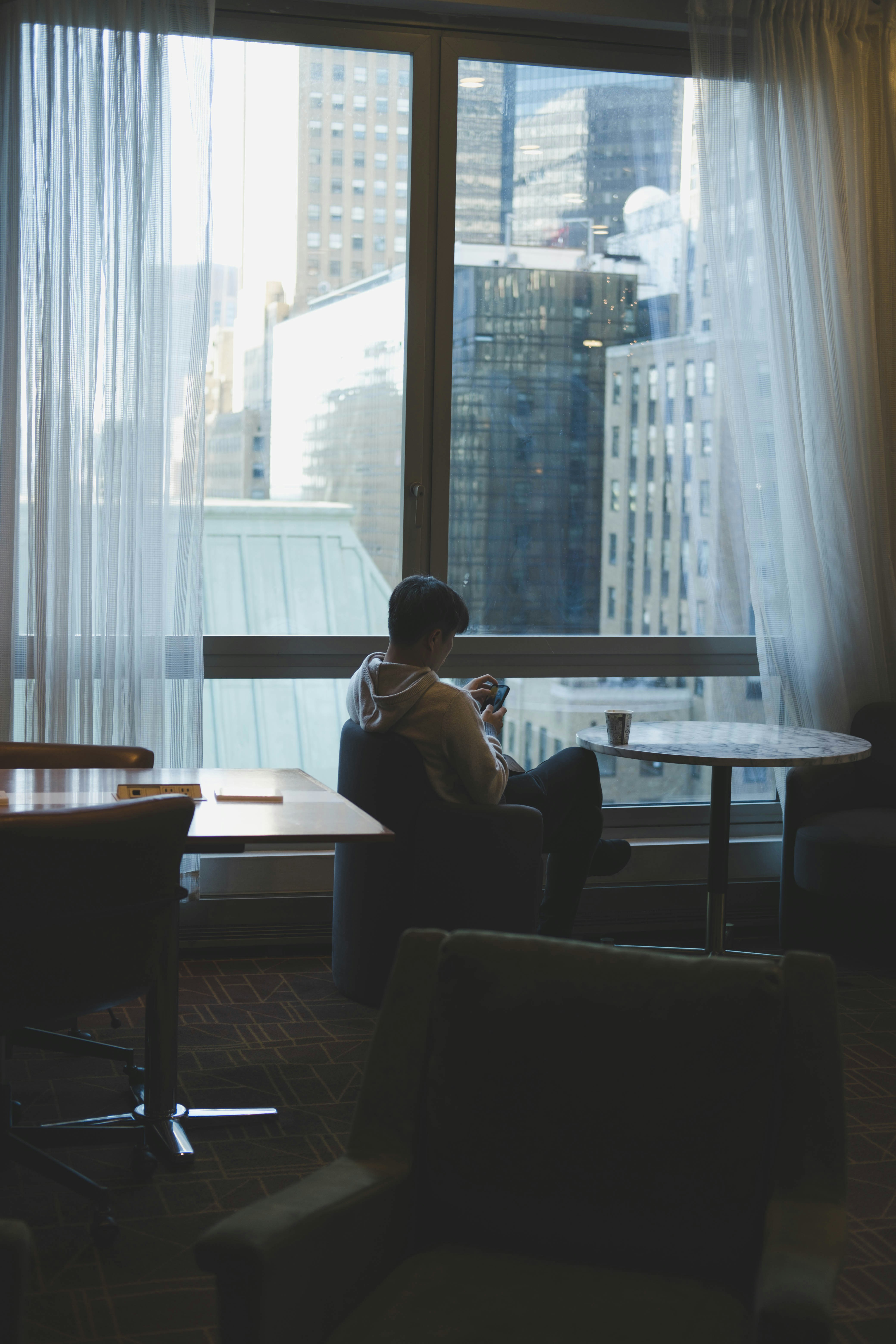 A person sitting in a chair looking out a window photo – Free Sitting ...