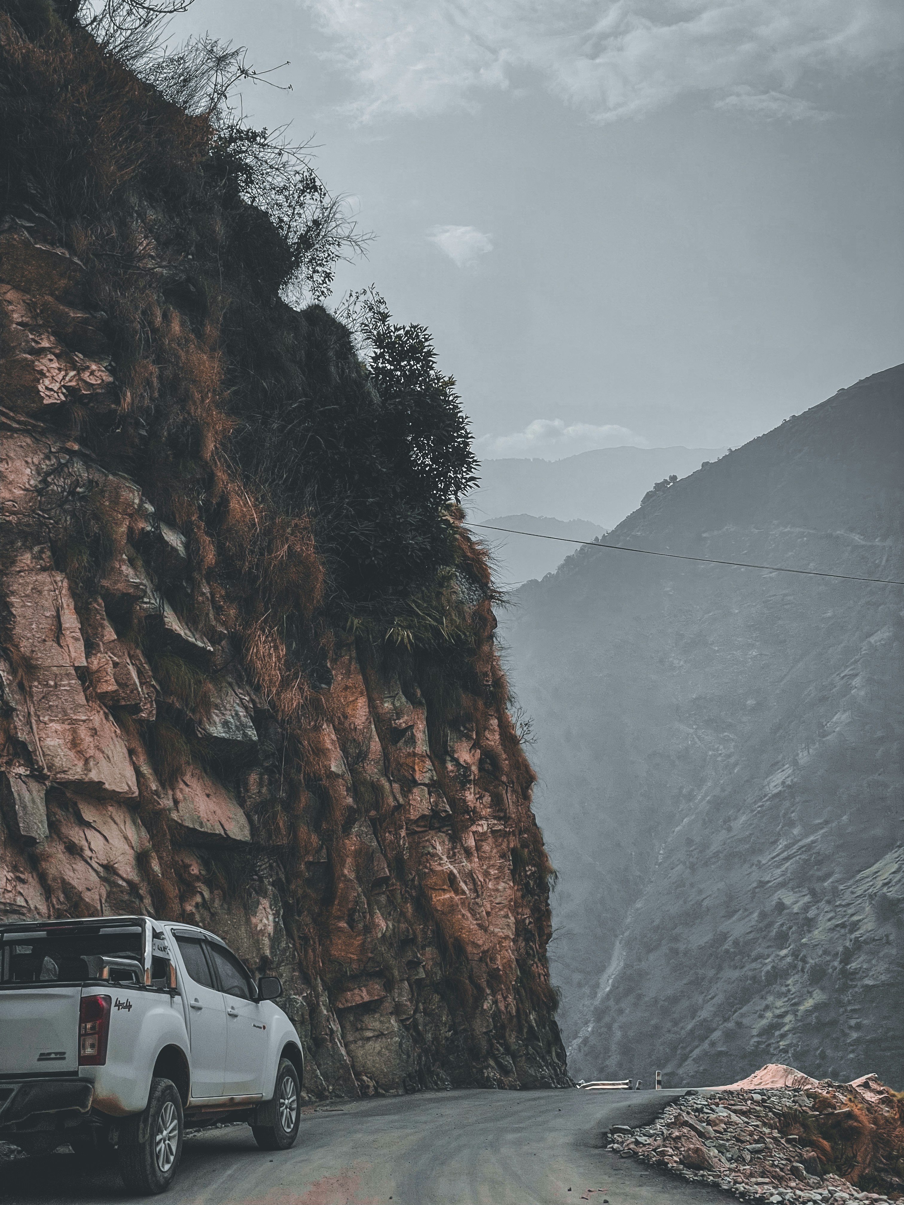 A rugged vehicle parked beside a steep rocky cliff, with mountains shrouded in mist in the background.