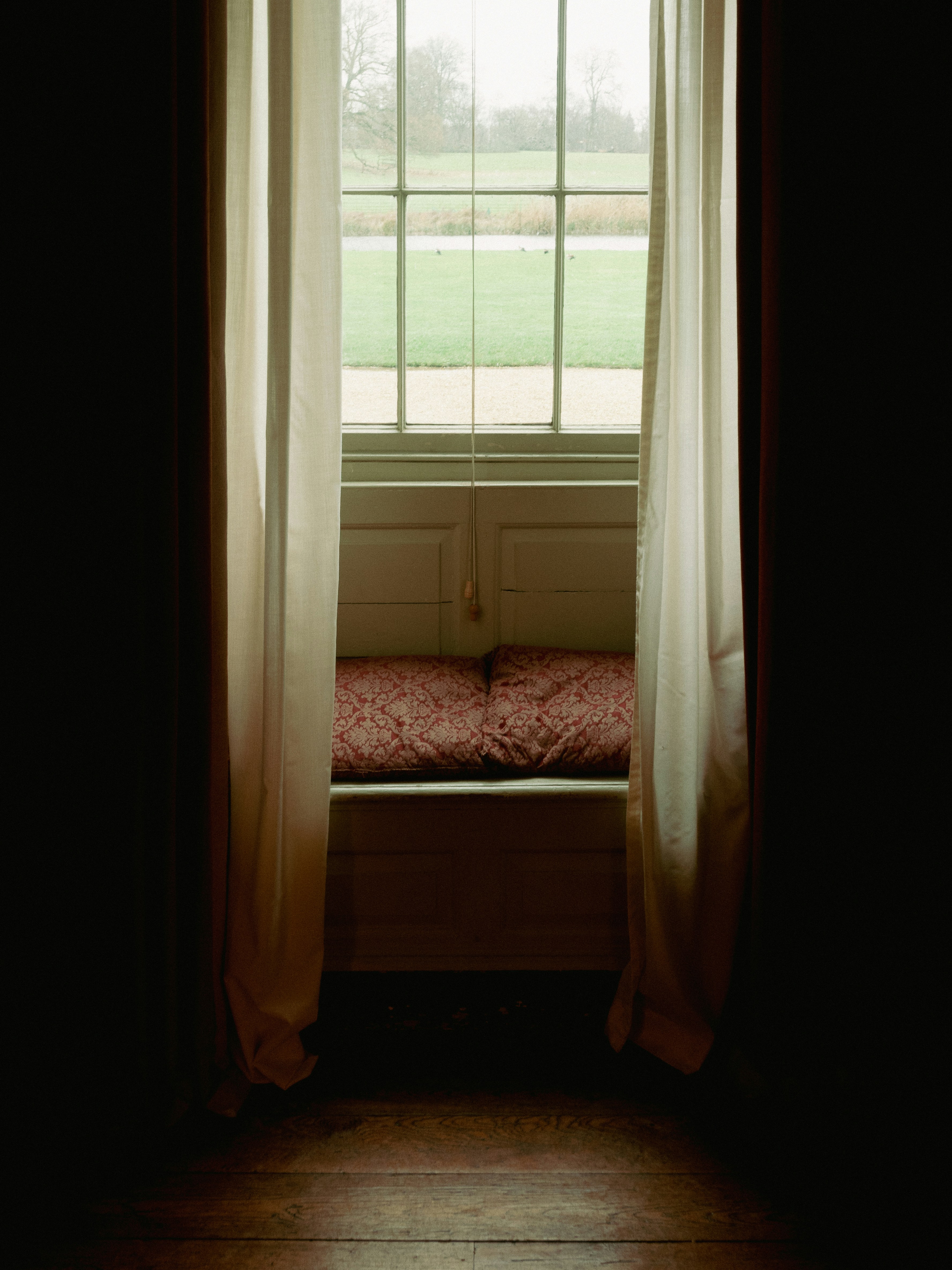 Soft curtains framing a window with a cozy seat, overlooking a serene green landscape. The ambiance invites tranquility.