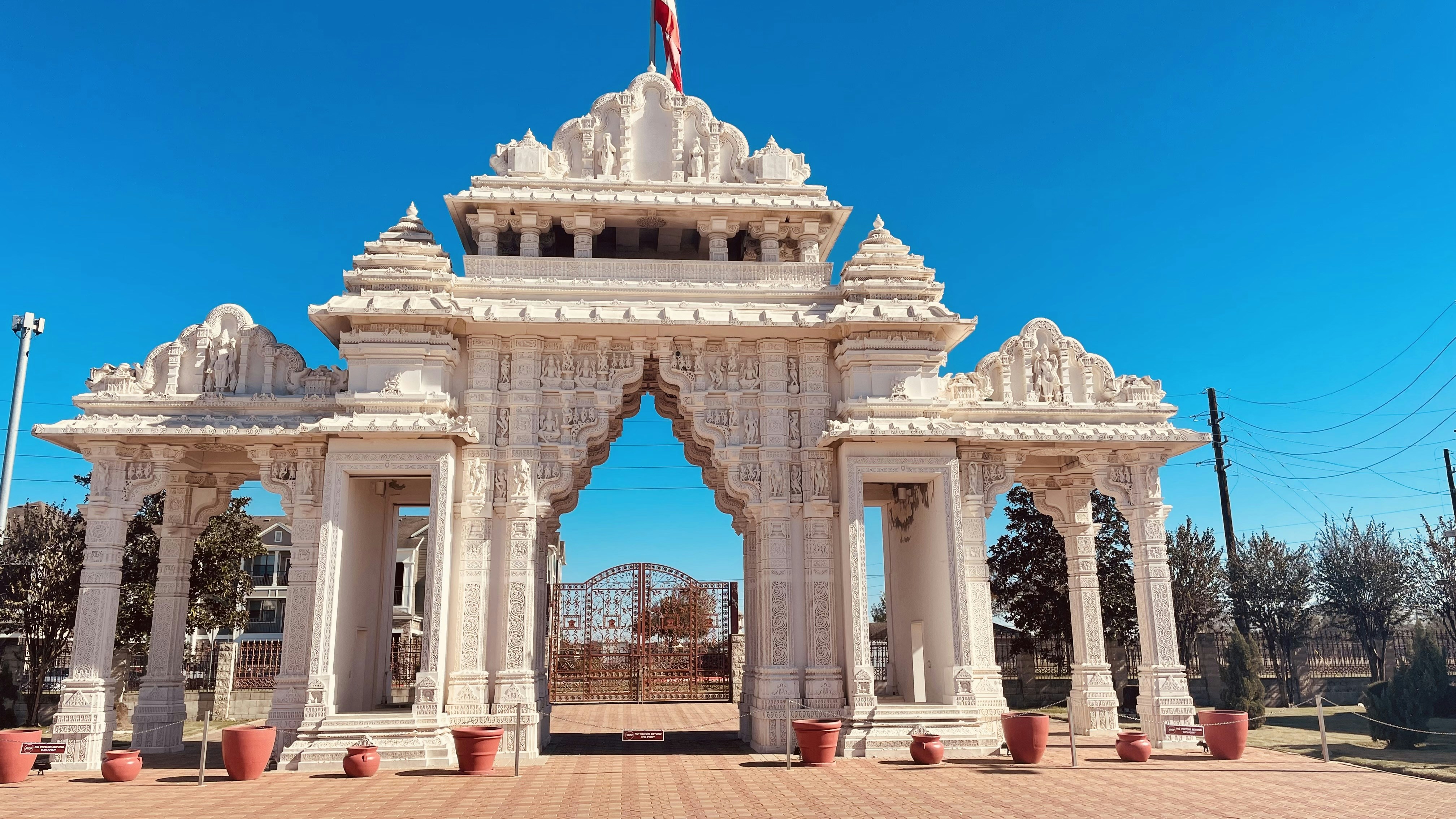 Ornate white temple entrance with a flag, set against a vivid blue sky.