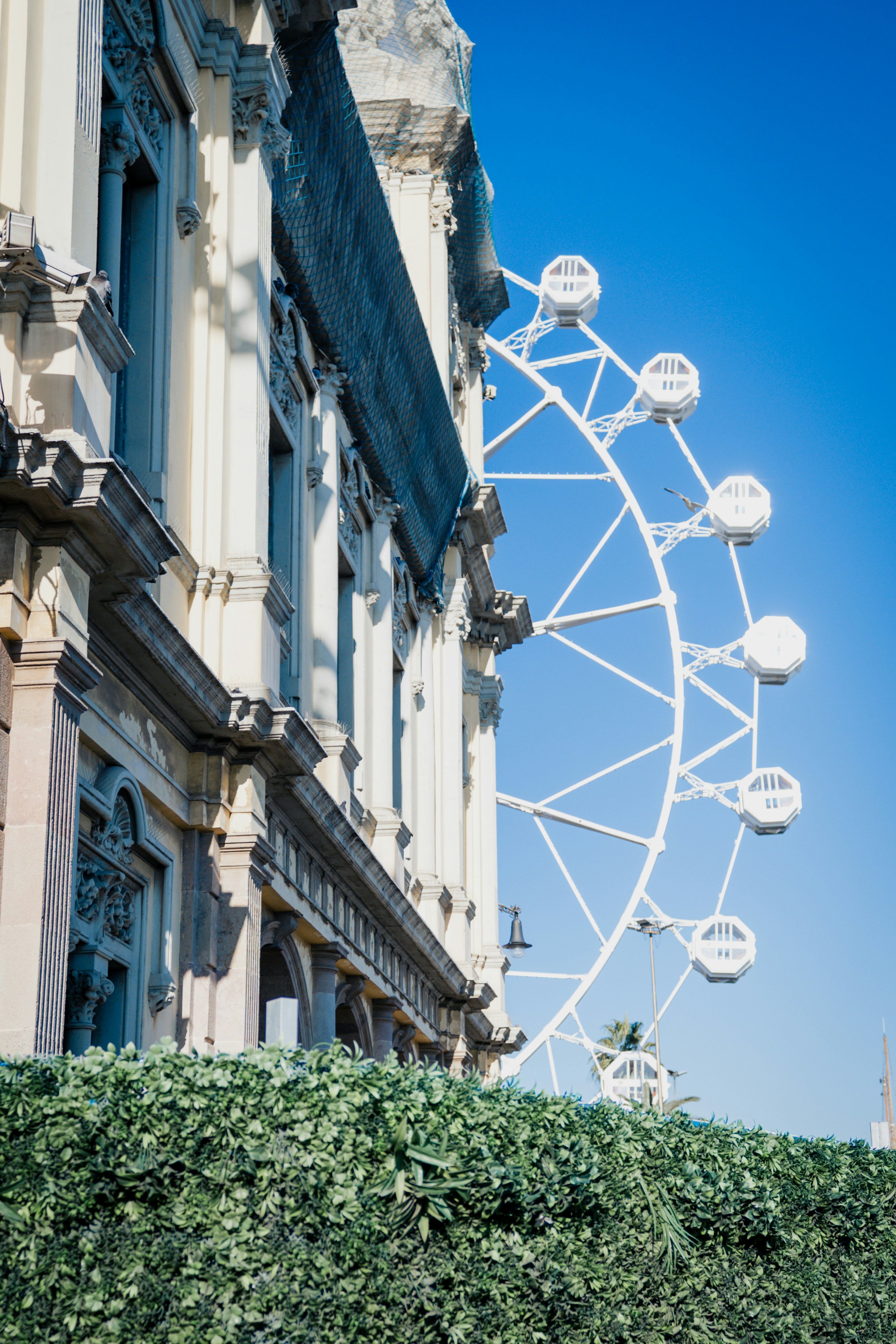 Stone Facade Framing a White Ferris Wheel Under a Clear Blue Sky