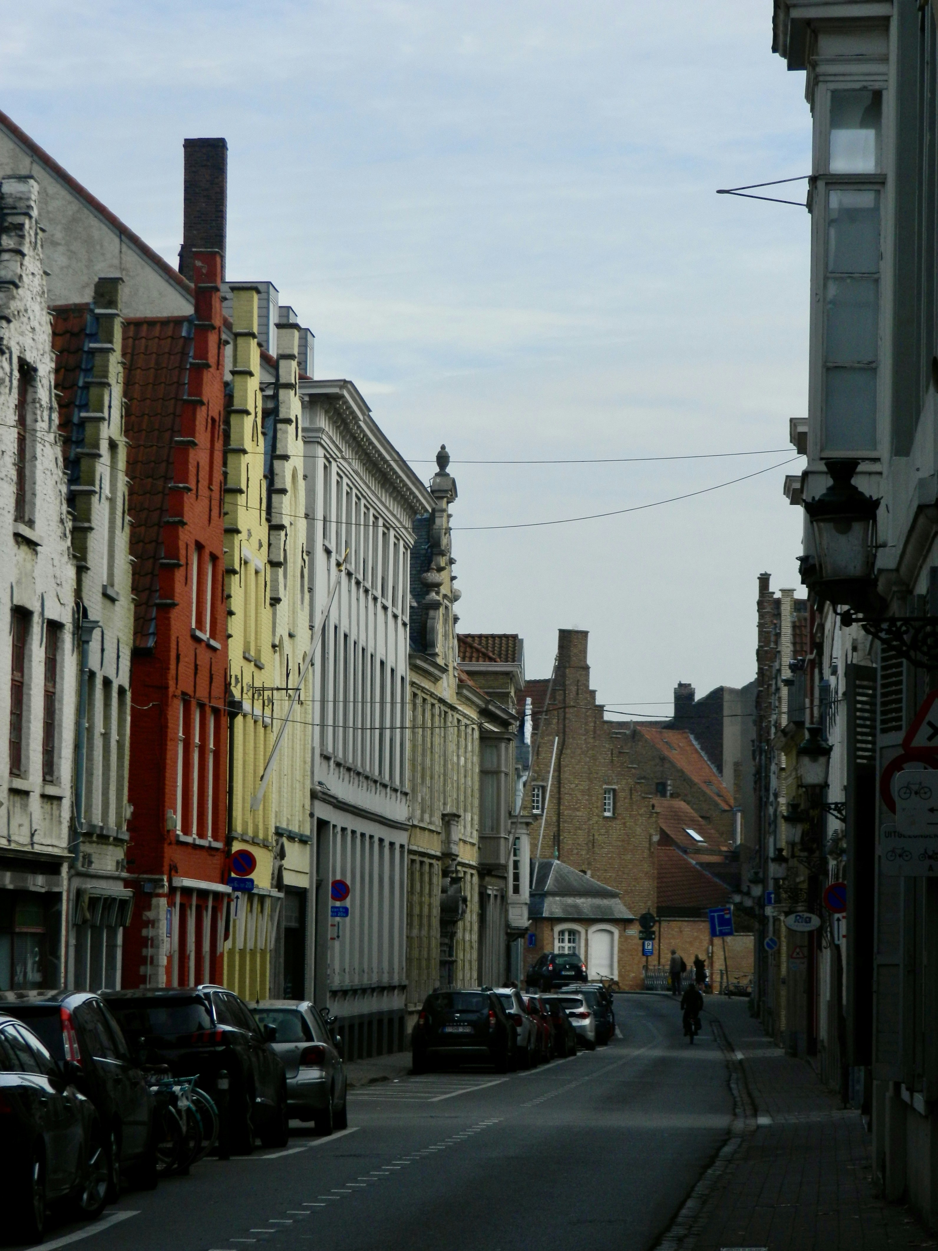 Narrow cobblestone street lined with colorful buildings, showcasing architectural diversity and a hint of urban life. A cyclist rides towards the end of the lane.