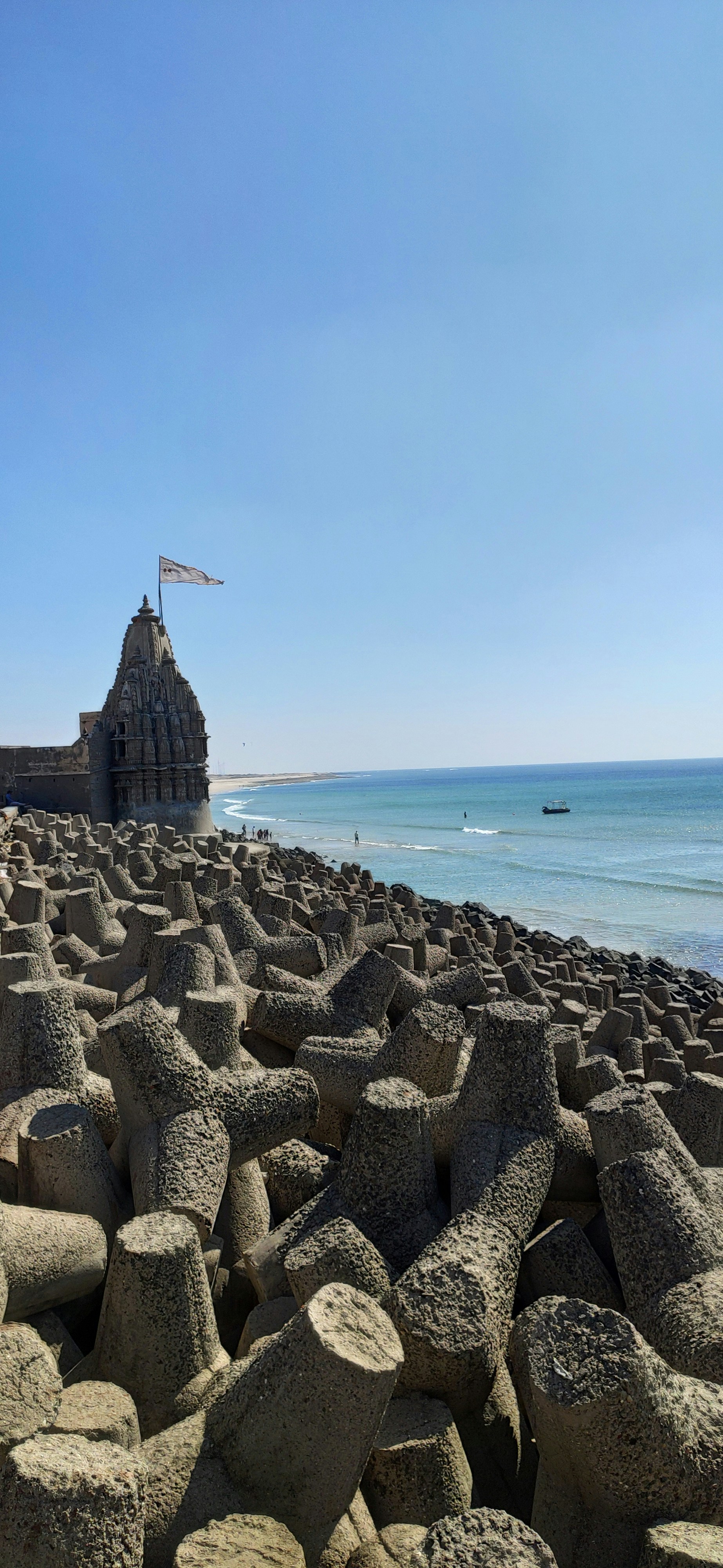 Temple overlooking a coastline with geometric concrete breakers under a clear blue sky.