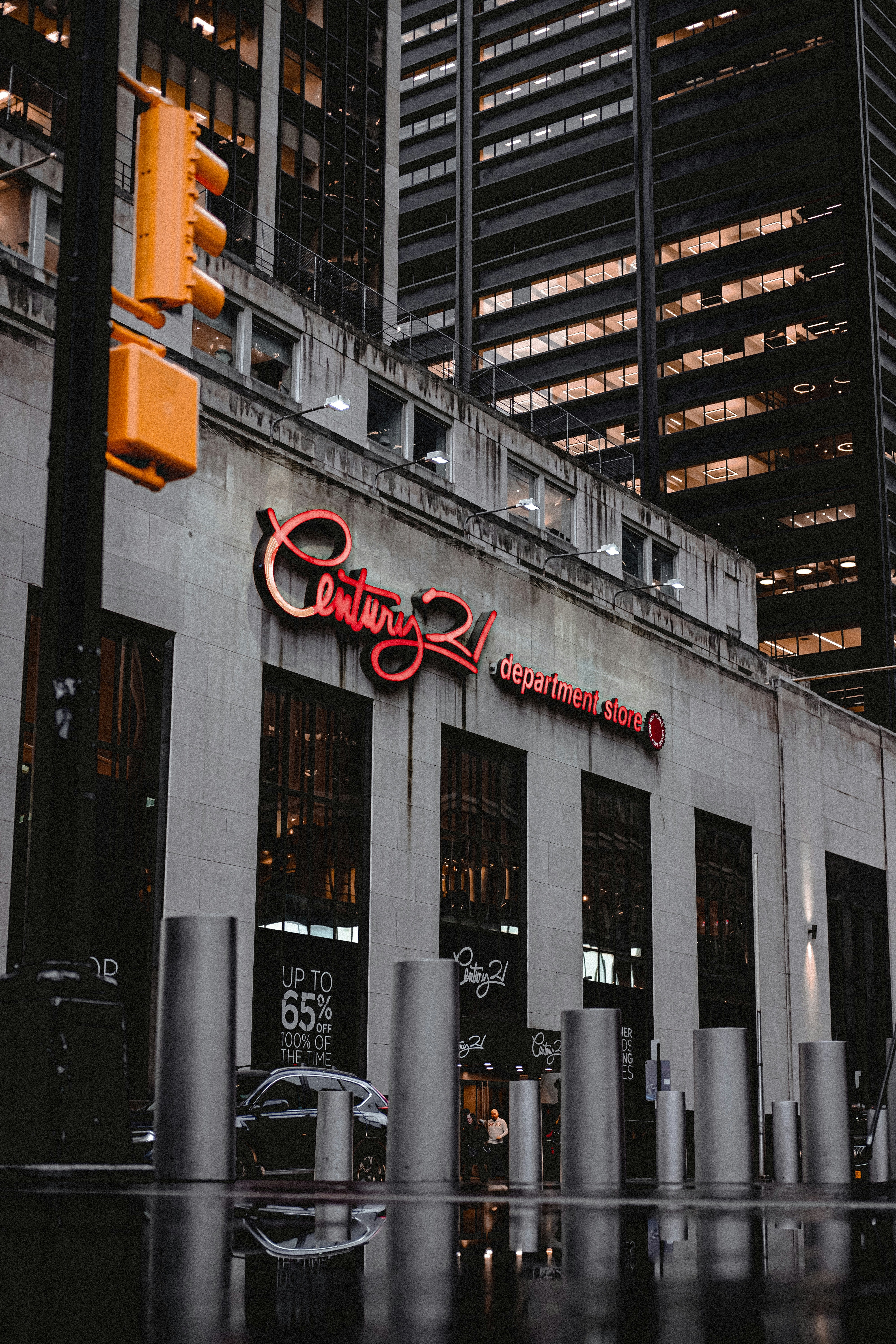 Century 21 department store illuminated in neon lights, showcasing reflections on a wet pavement amidst towering skyscrapers.