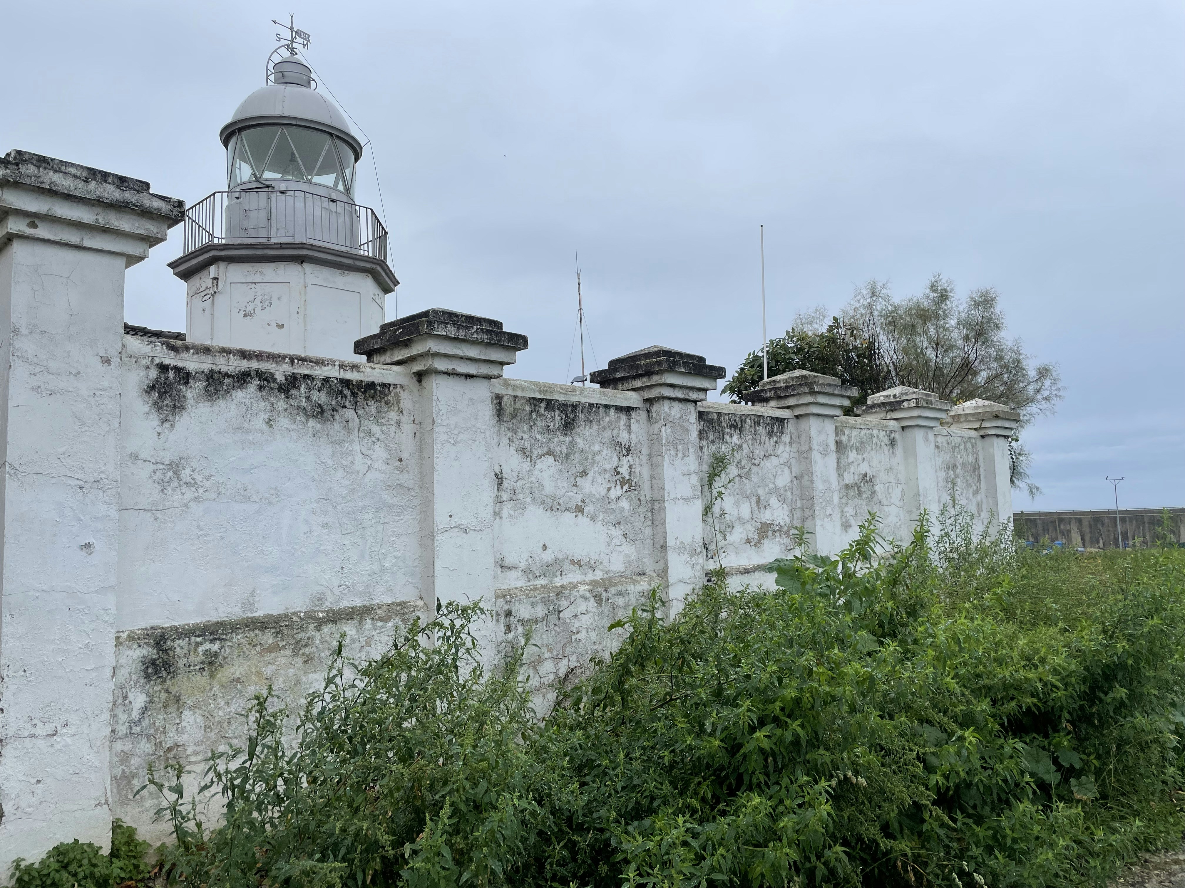 Beacon Beyond the Wall: A Weathered Lighthouse Framed by Verdant Boundary