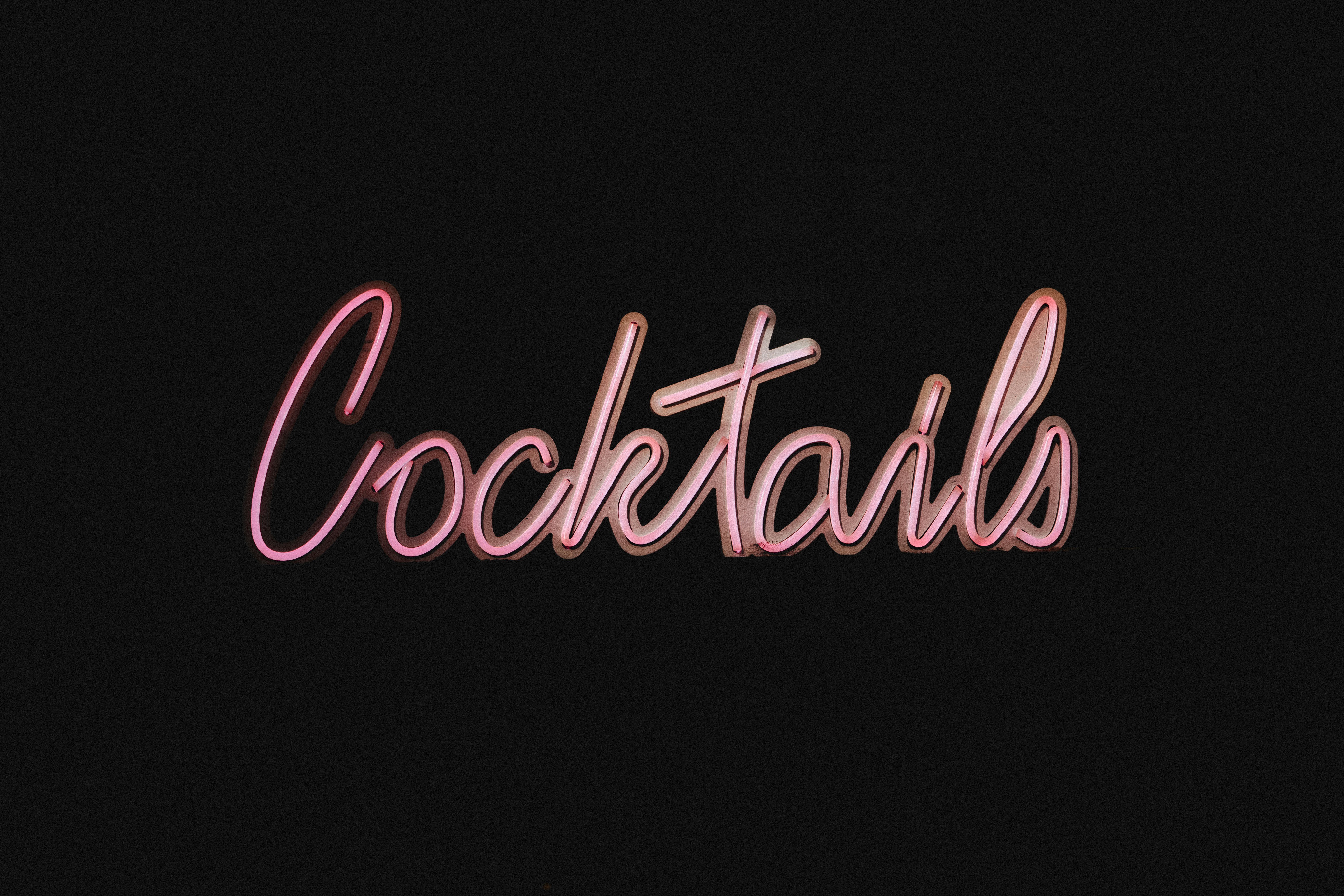 Vibrant neon sign spelling 'Cocktails' against a dark background, emphasizing the allure of mixology.