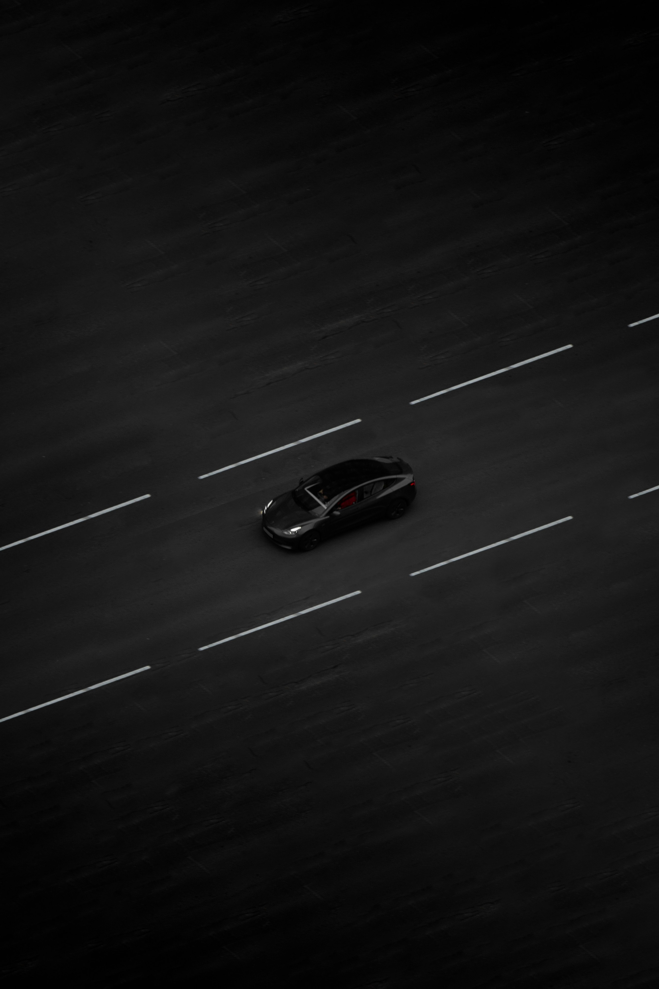 A sleek black car speeds down a dimly lit highway, flanked by stark white lane markings. The contrast creates a striking visual of urban movement.
