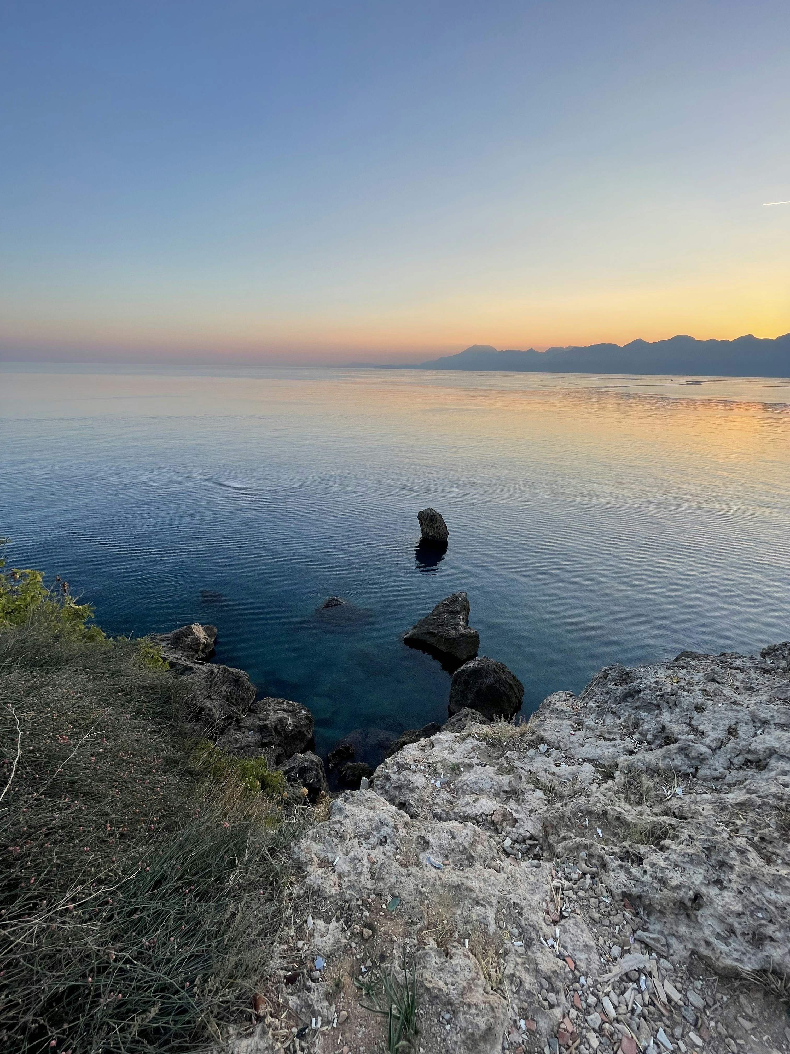 Sunset Over Quiet Waters: A Rocky Shore Forefront Overlooking a Calm Sea