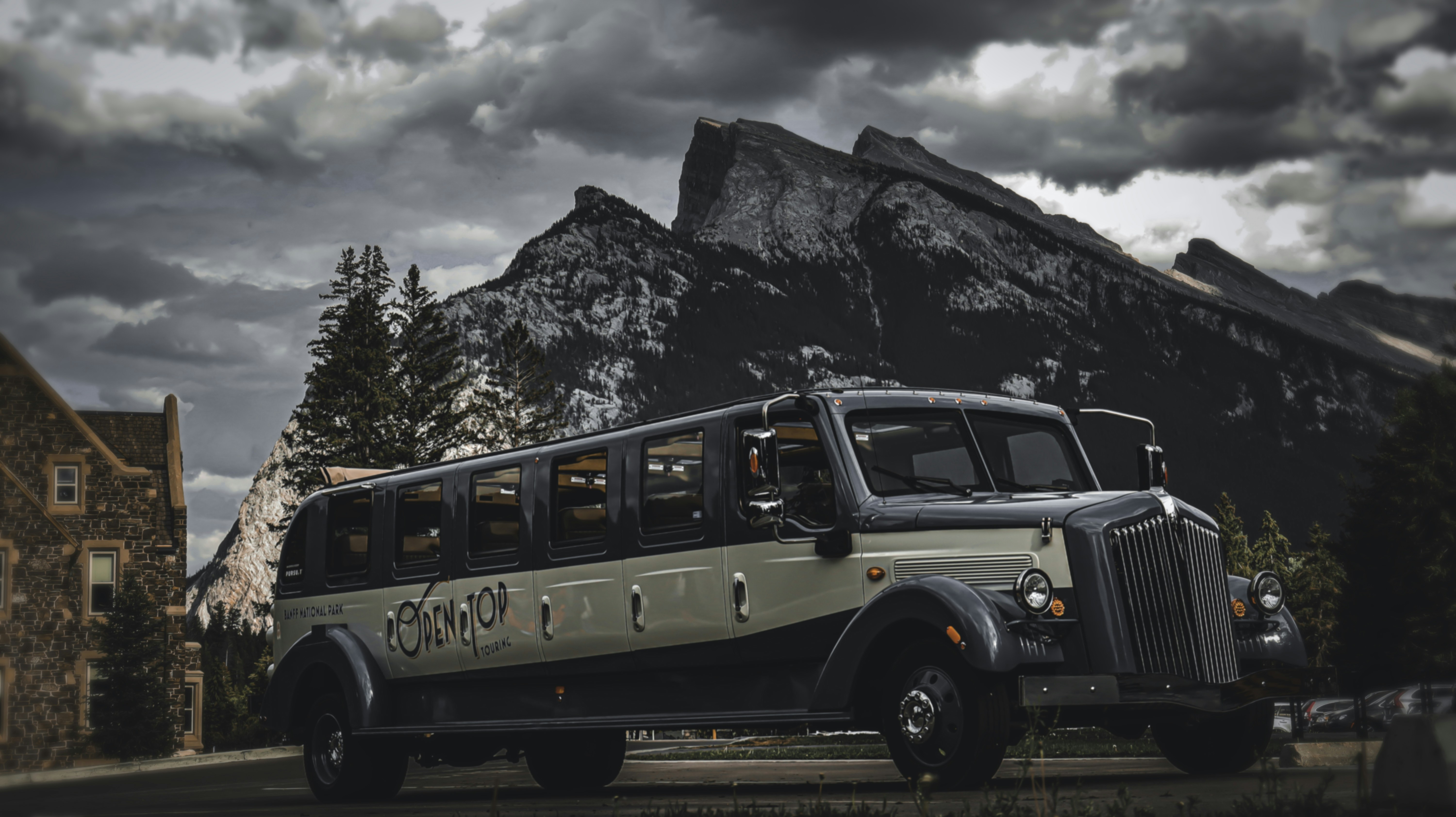Black-and-white photograph of a vintage coach parked before jagged mountains under a dramatic sky.