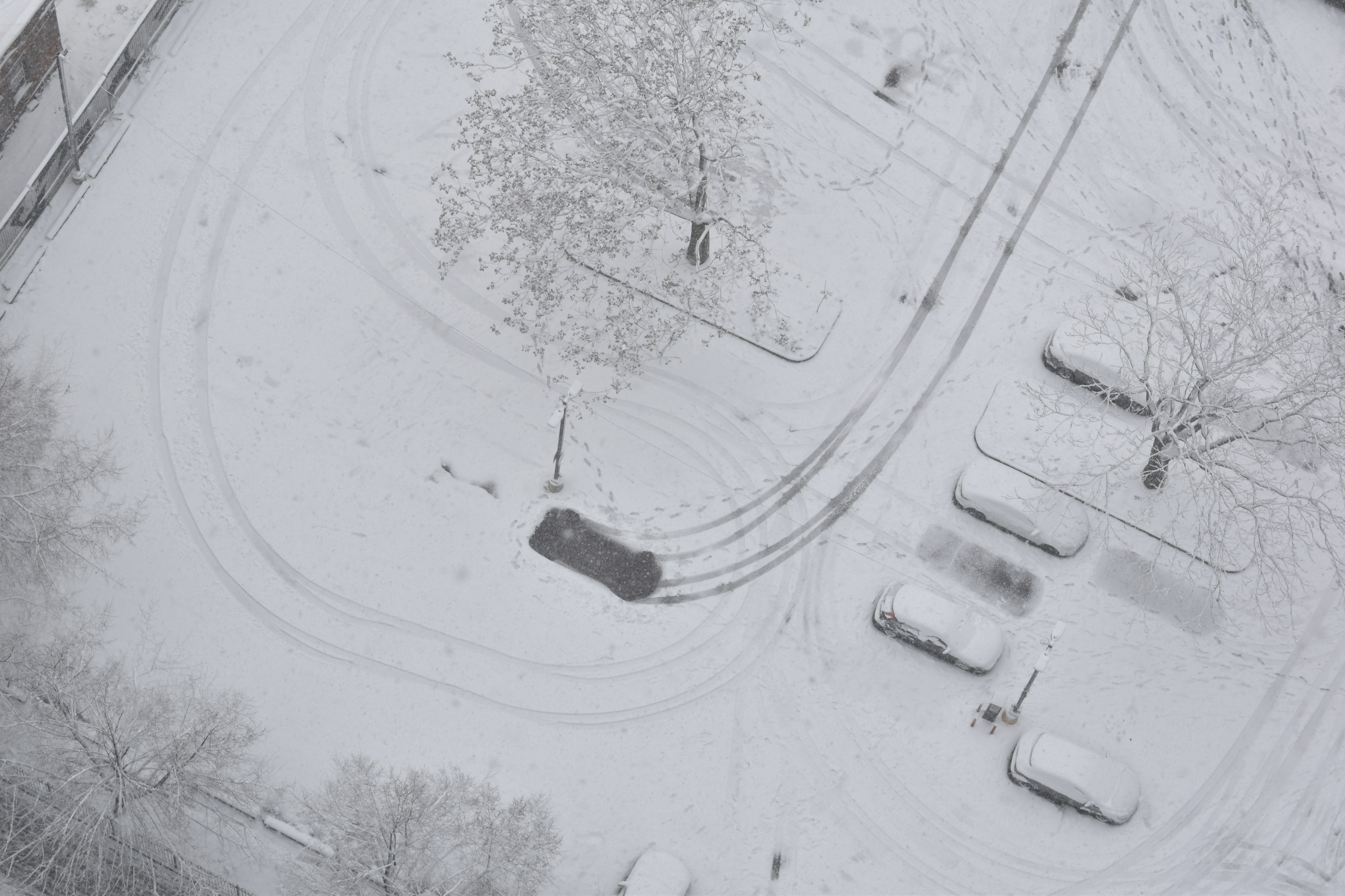 Aerial view of a snow-covered parking area and circular park path with a central feature and bare trees.
