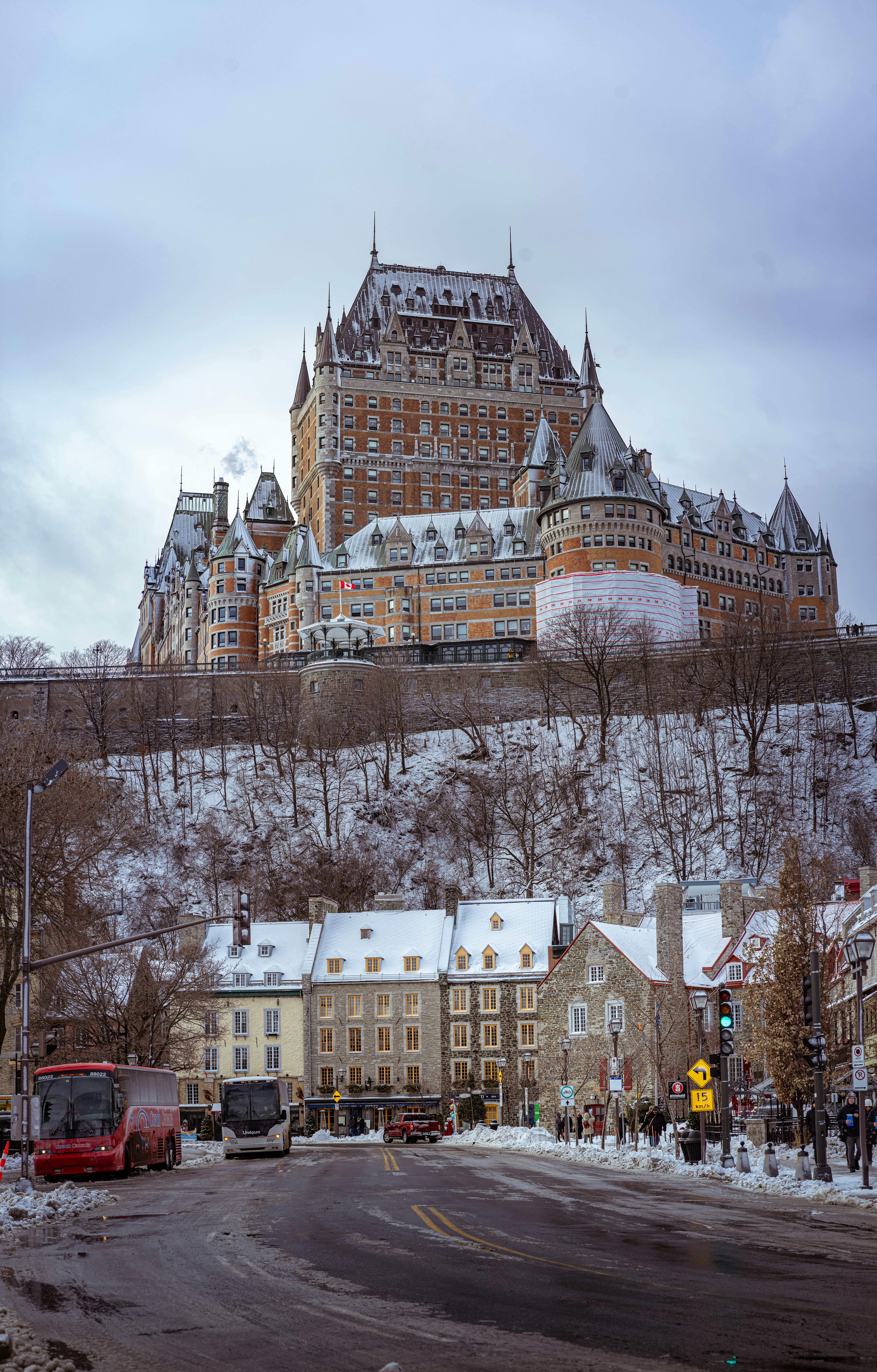 Historic Château Frontenac towers over a snow-covered street in Quebec, showcasing its architectural grandeur against a cloudy sky.
