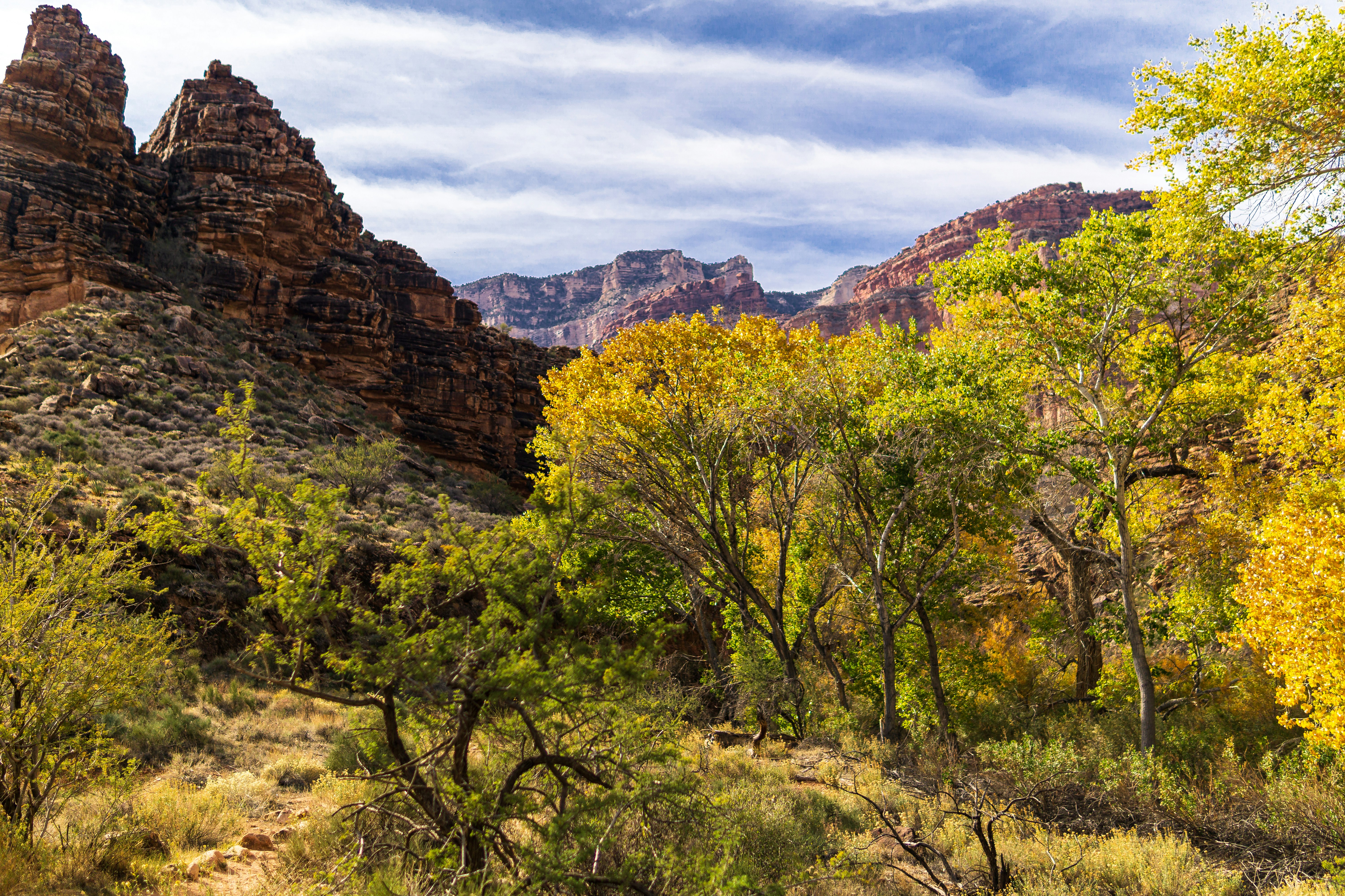 Vibrant autumn foliage contrasts with rugged brown cliffs under a partly cloudy sky.