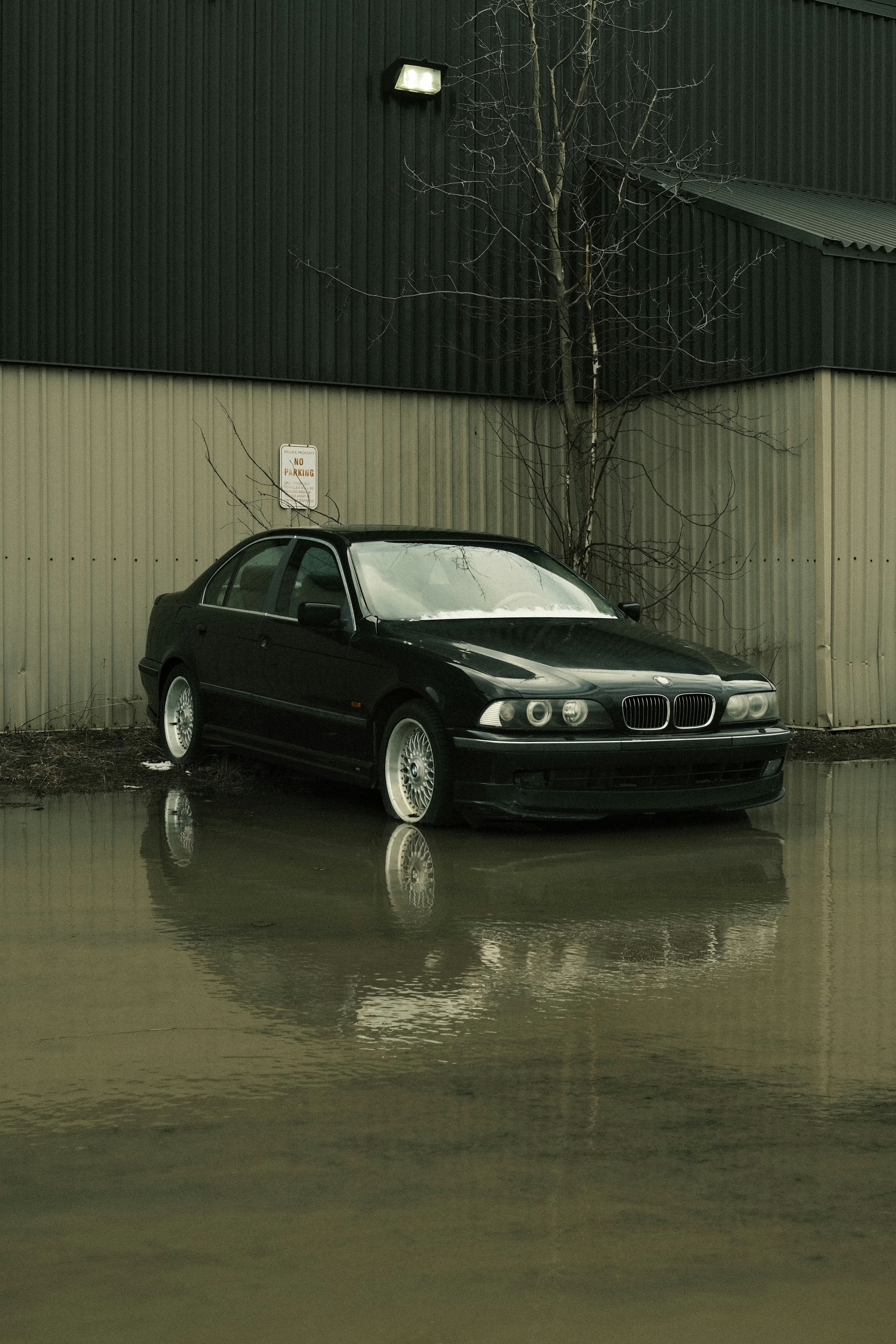 Mirror Water, Silent Sedan: A Black BMW Resting in a Flooded Parking Lot