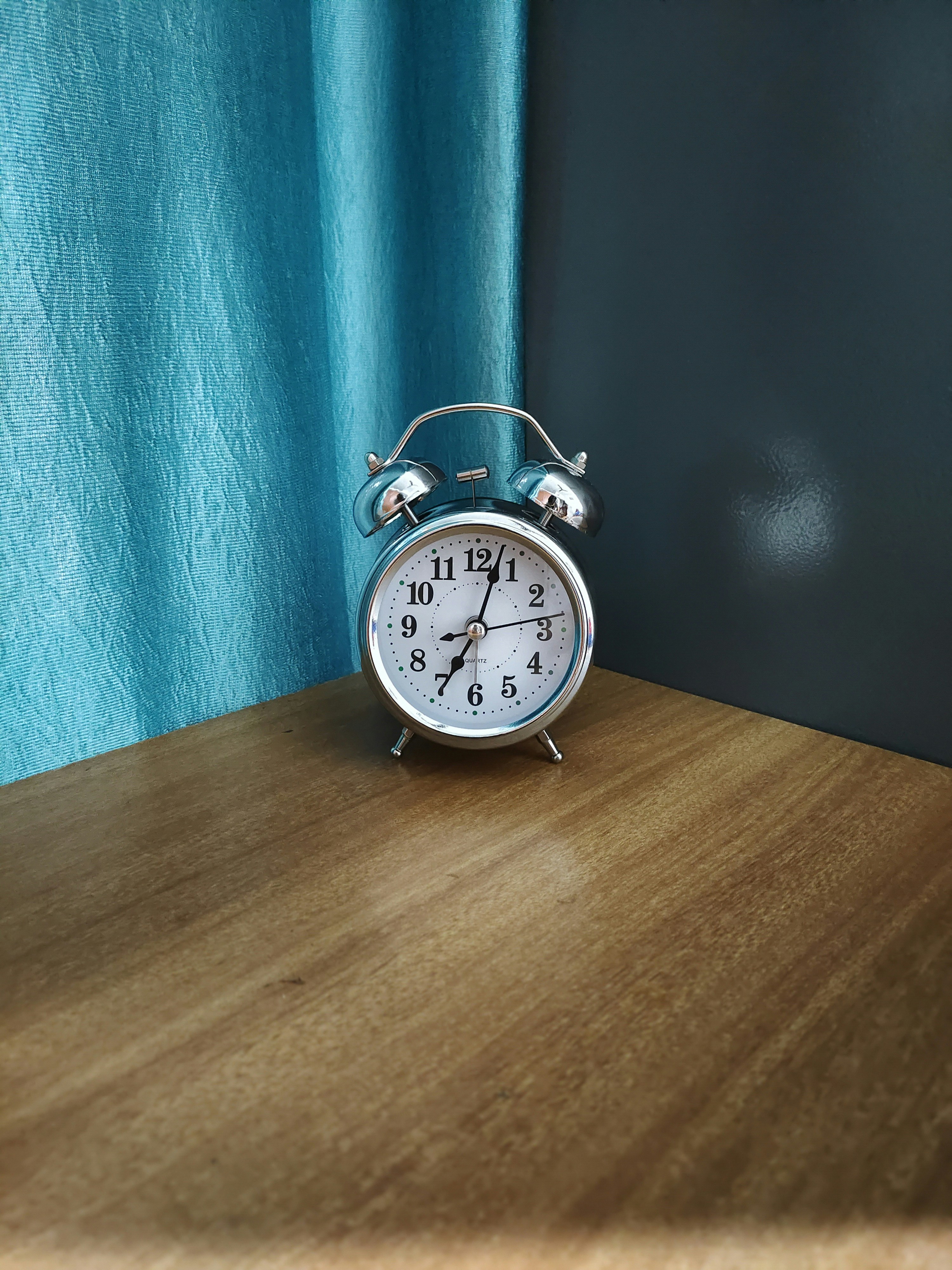 Silver Alarm Clock on Wooden Desk with Teal Curtain